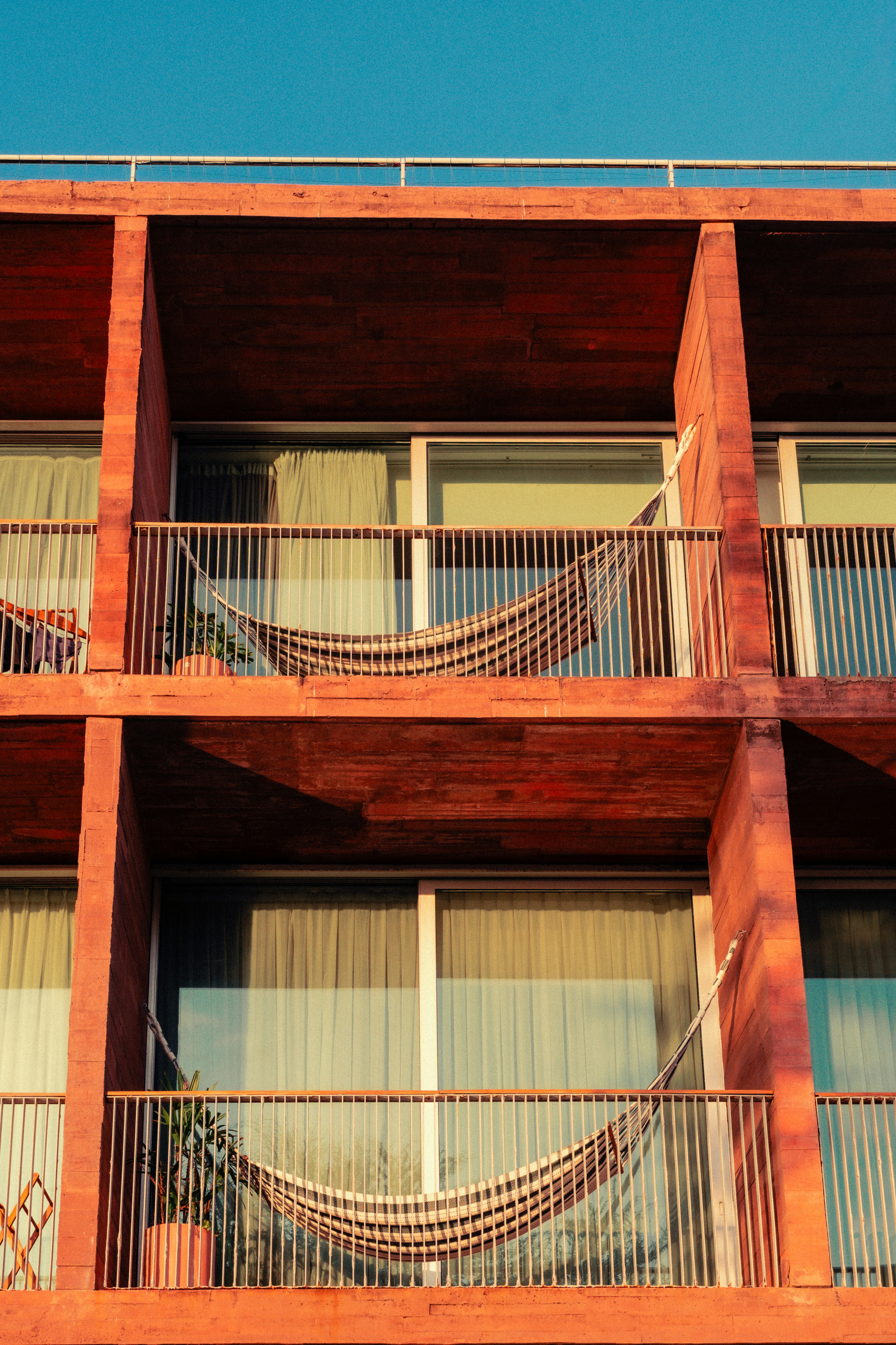 Red brick balconies with hanging hammocks and glass doors, bathed in warm afternoon light on a modern apartment building.