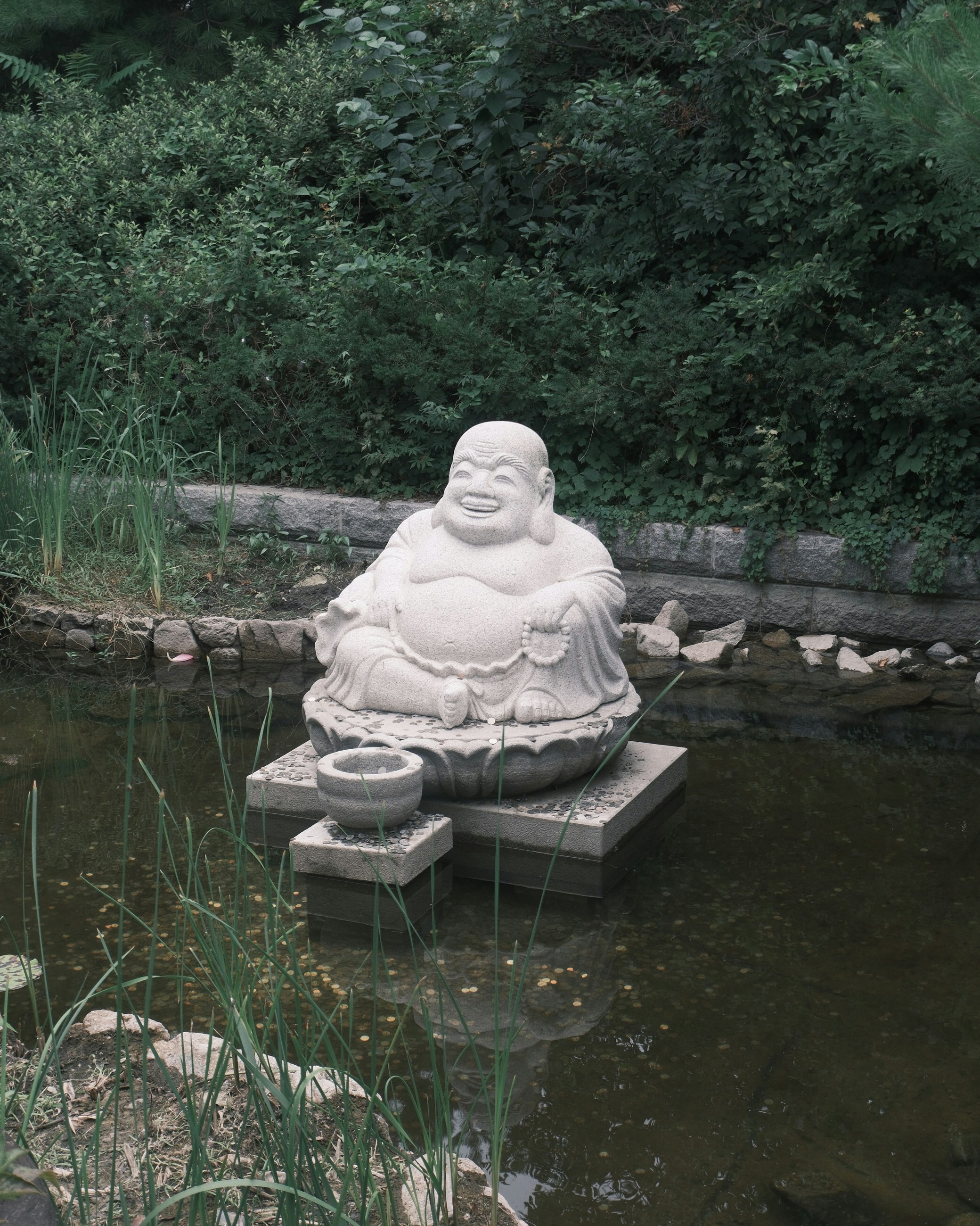 Laughing Buddha on a Stone Platform Surrounded by Water and Greenery