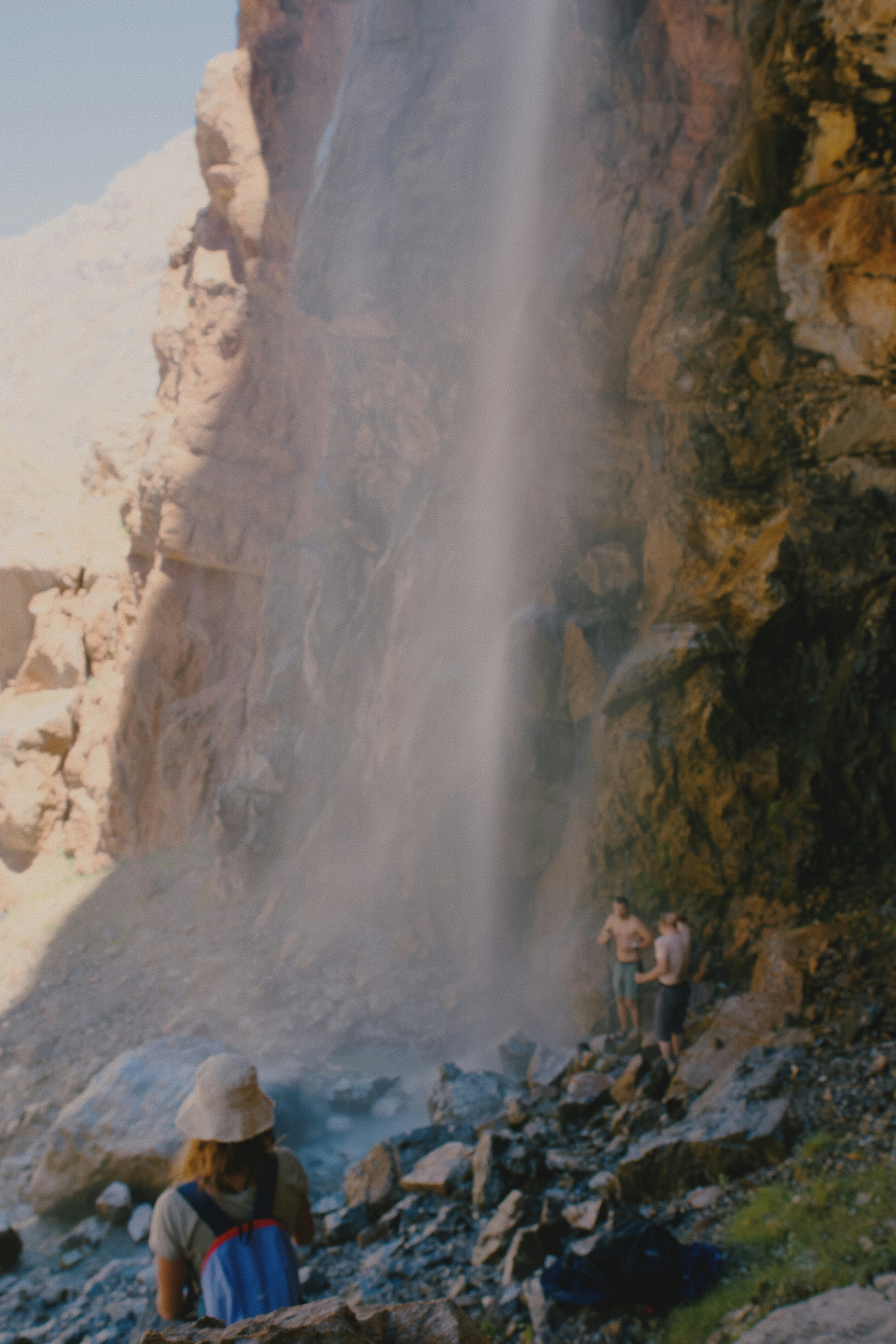Mist Veil by the Canyon: Hikers at the Base of a Soaring Waterfall