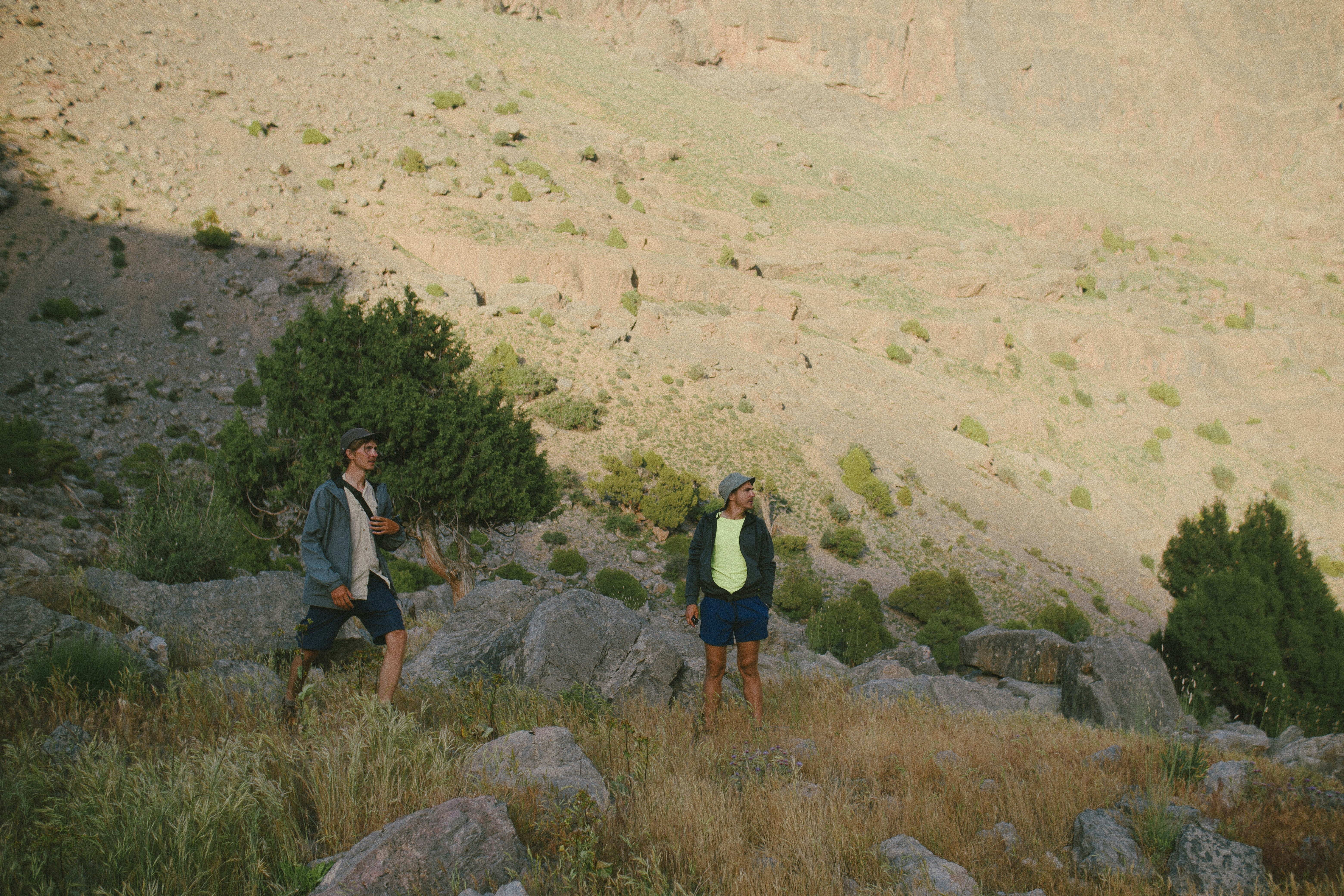 Two hikers pause among rocks with a sunlit canyon backdrop