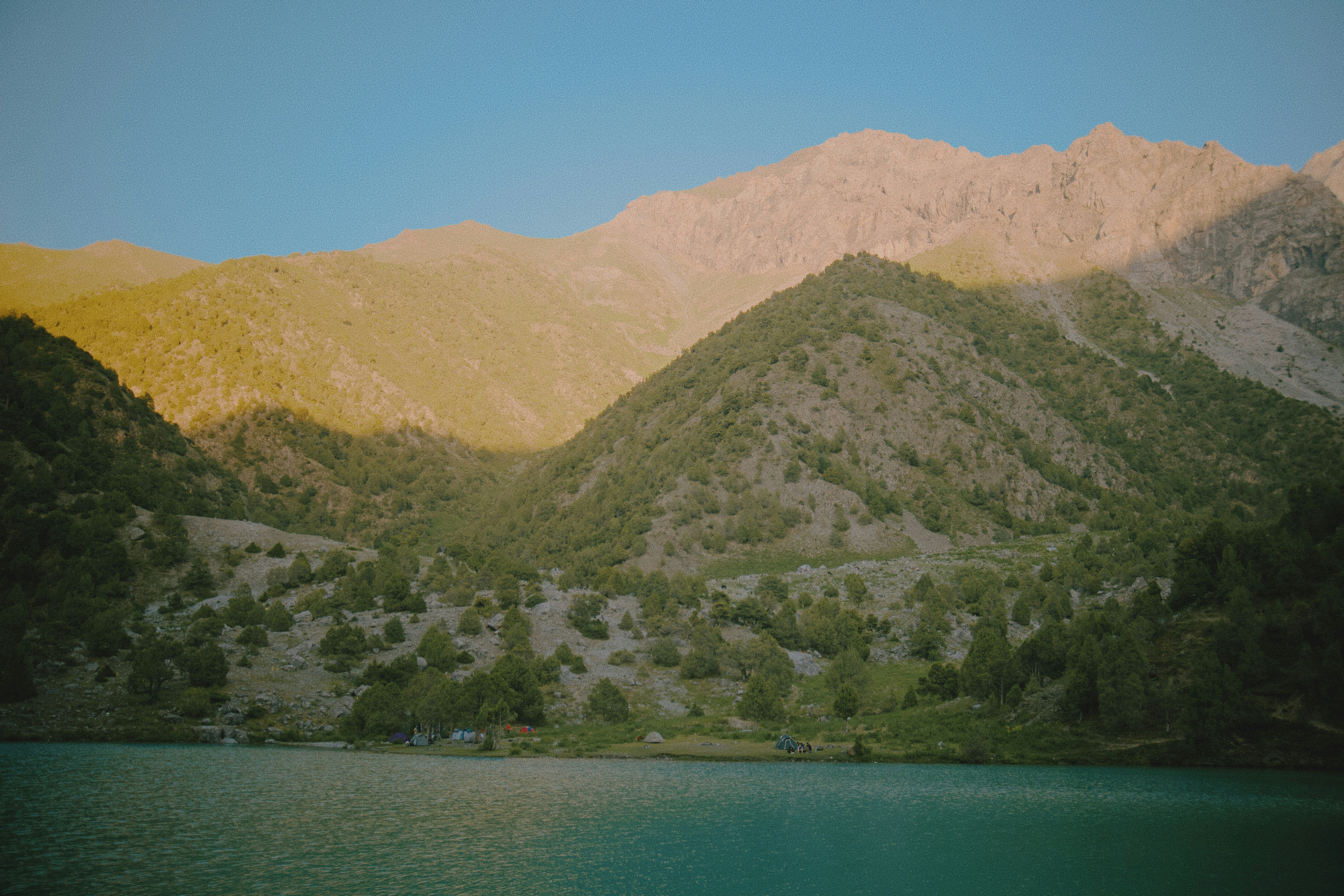 A turquoise mountain lake with small tents on the shore below rocky peaks