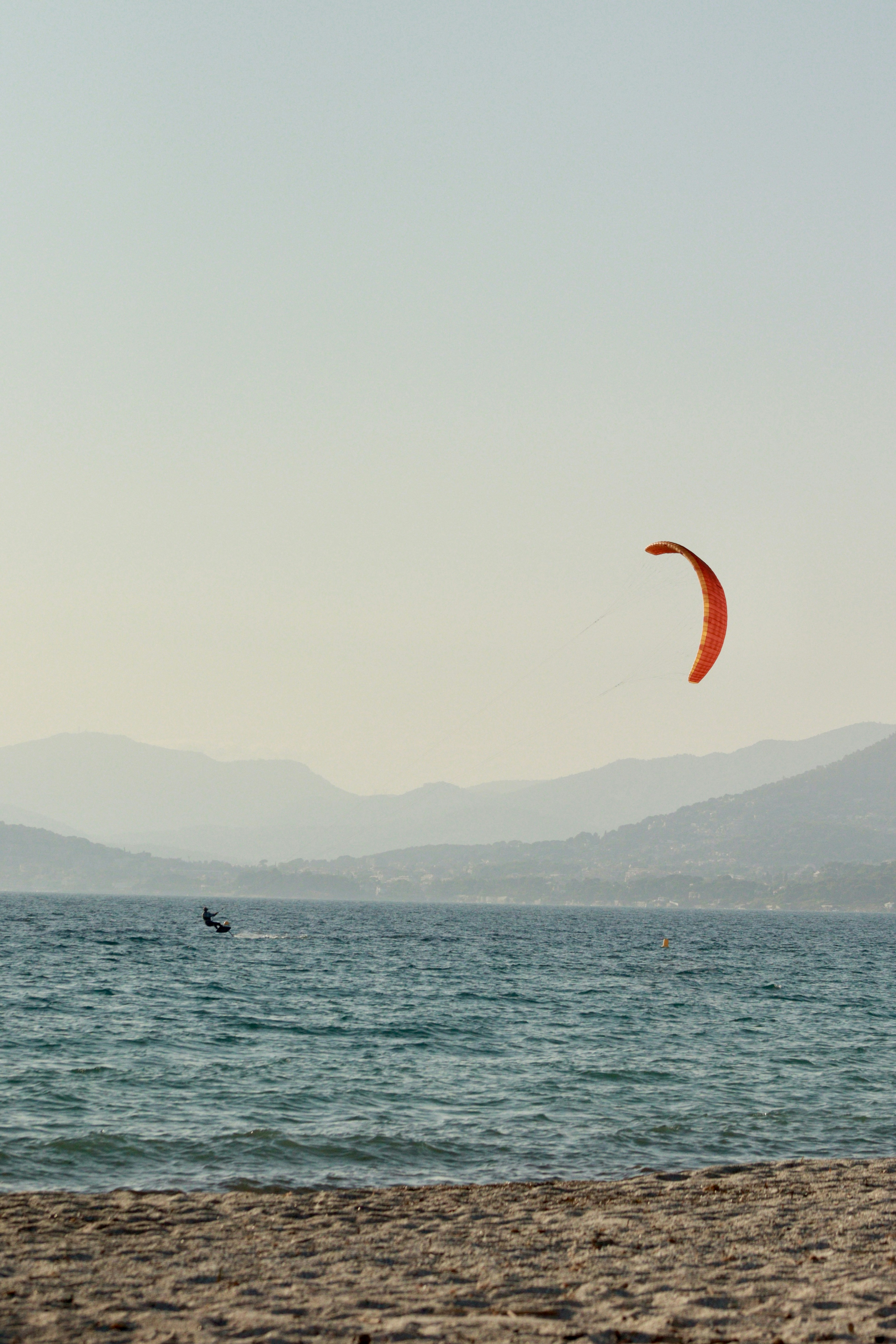 Sail and Sky: A Red-Parachute Kite Over Quiet Seascape