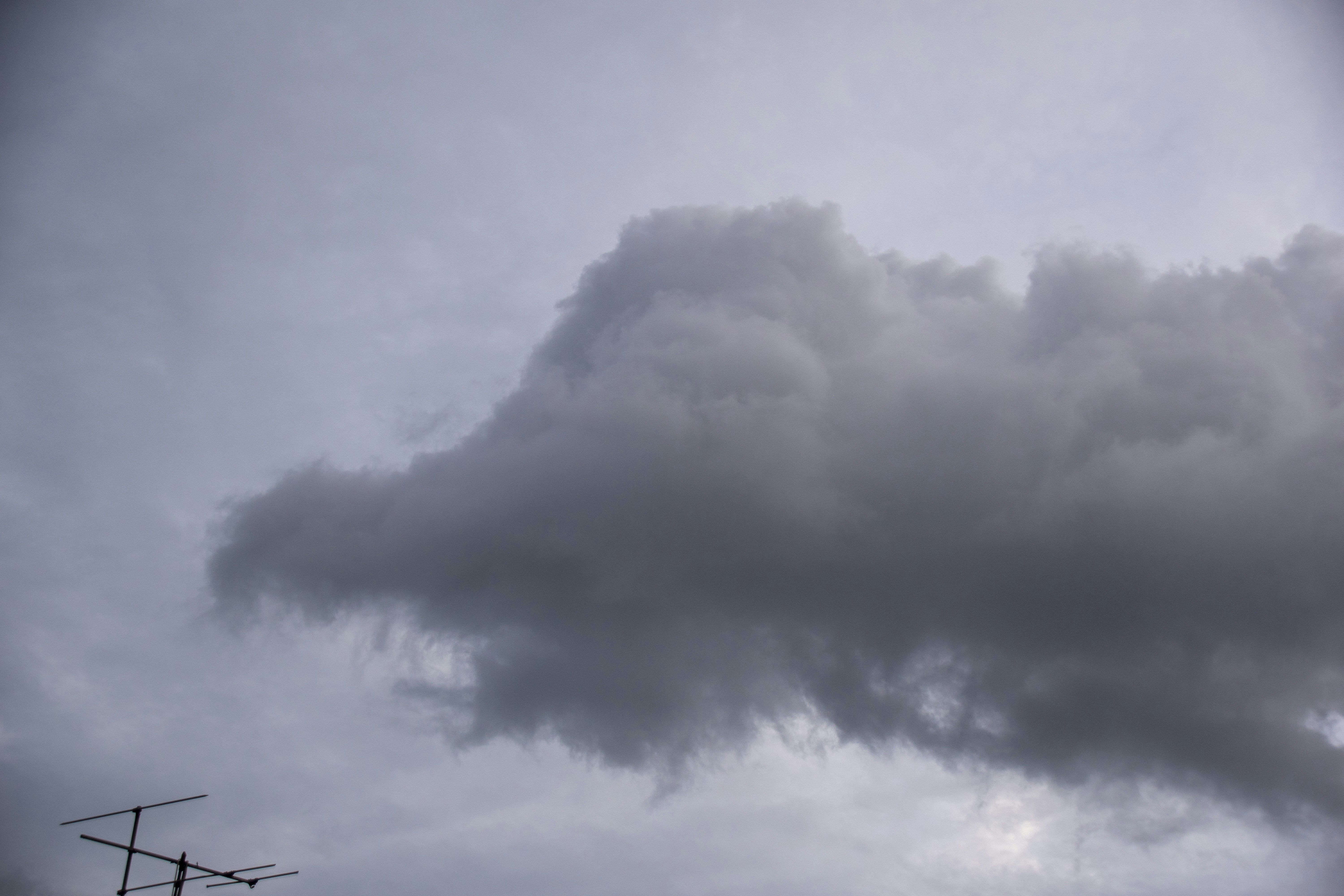 Low-angle sky with a dense cloud drifting above rooftop antenna silhouettes, emphasizing moody atmospheric tones.