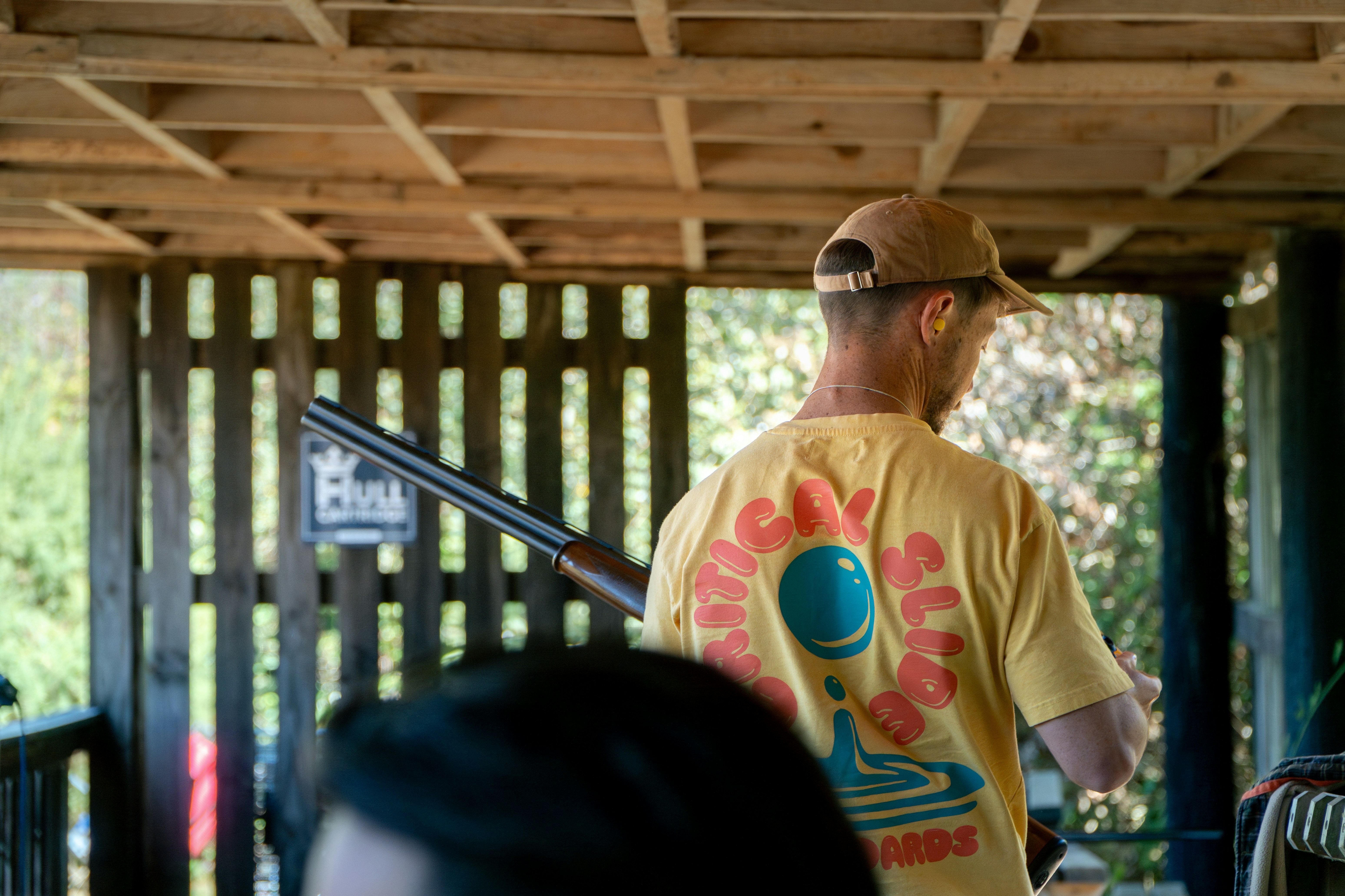 Sunlit batter in a rustic practice shed: a batterman in a yellow tee aims a shade-arrowed bat