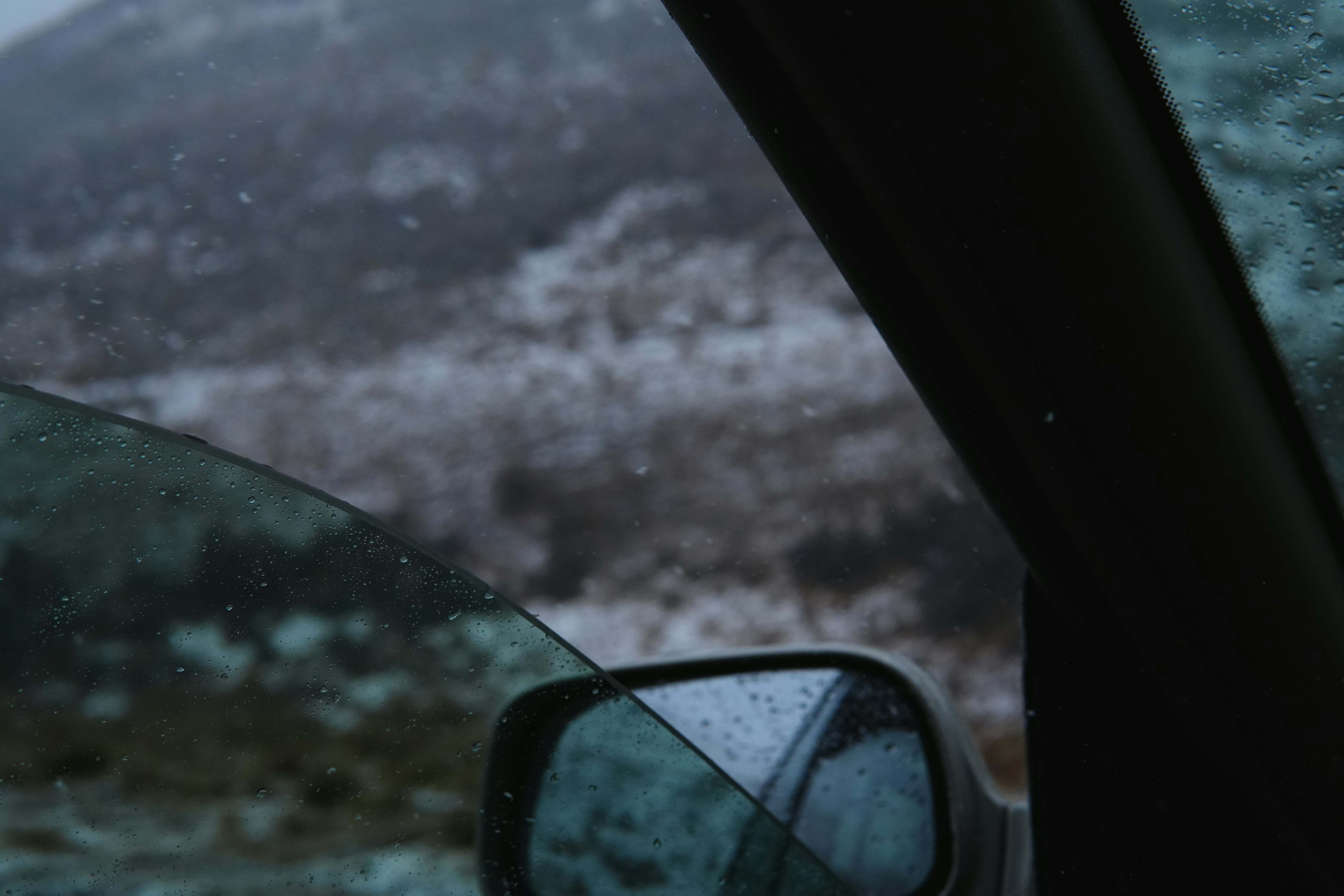 Rain-kissed car window with side mirror reflection at dusk