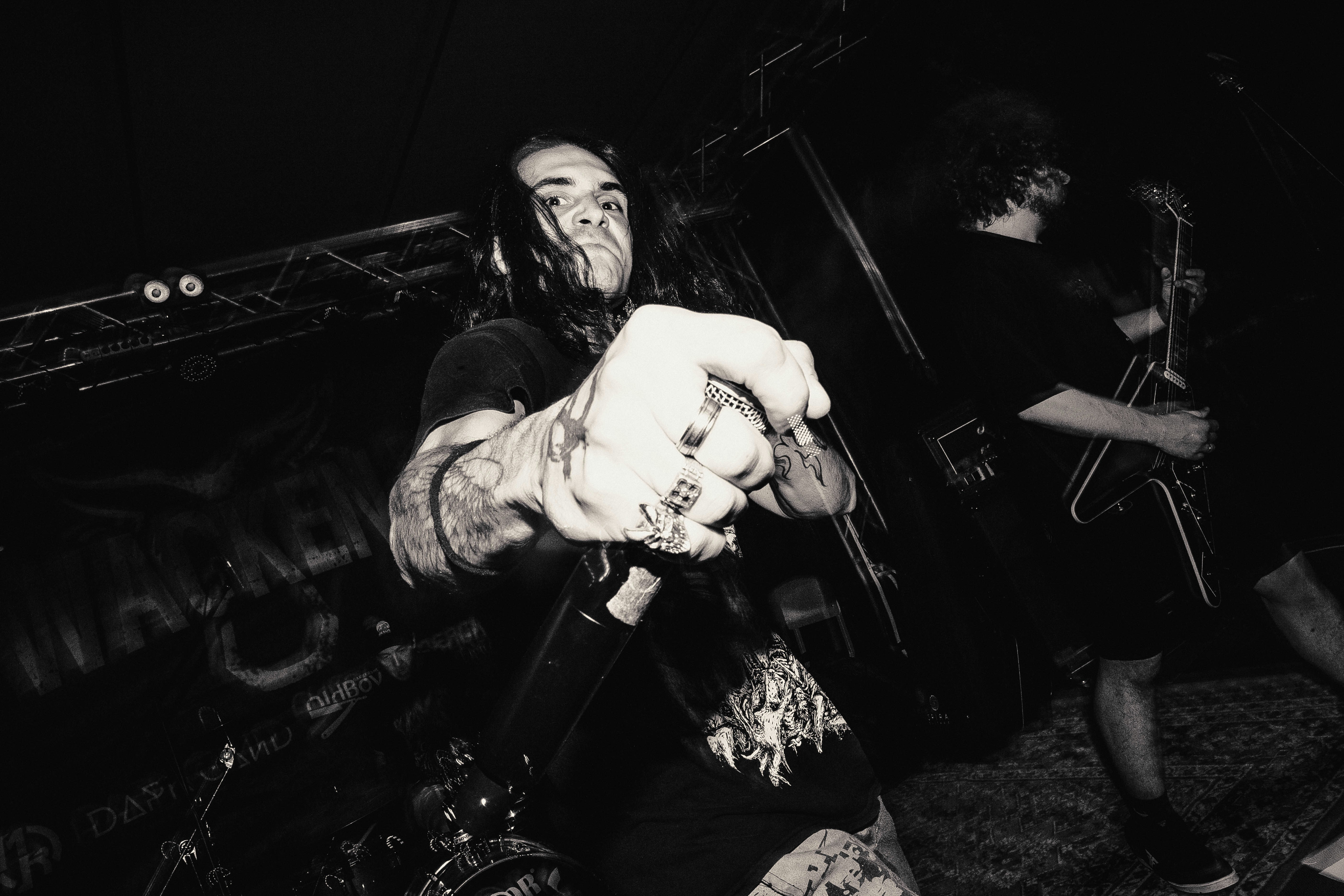 A black-and-white concert moment focusing on a guitarist lunging toward the camera, with another musician in the background; the scene captures raw energy and stage lighting in a live venue.