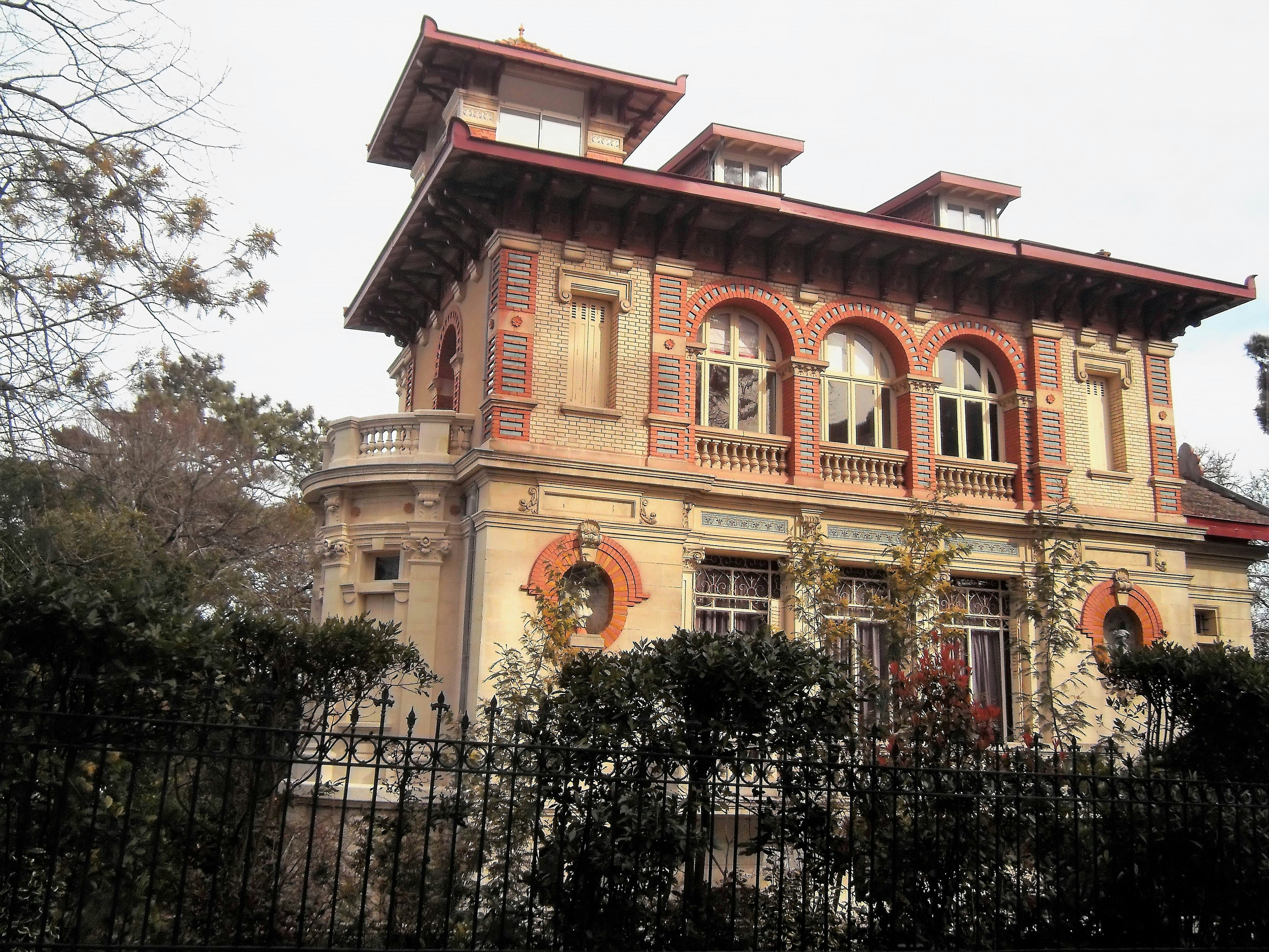 A historic brick and stone villa with arched windows behind a black iron fence