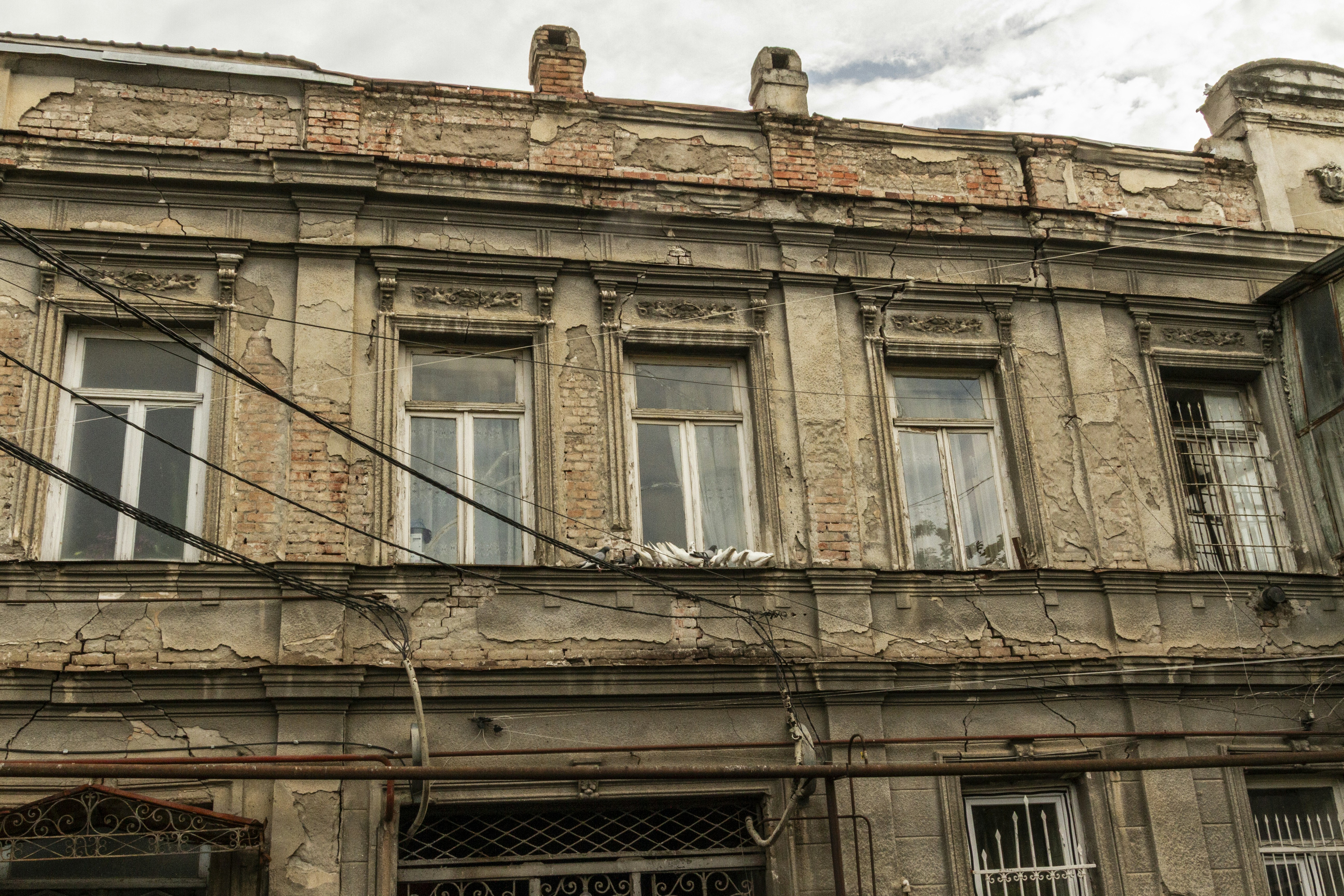 Old brick-and-plaster building facade with decorative window frames and tangled overhead wires in a muted urban scene.