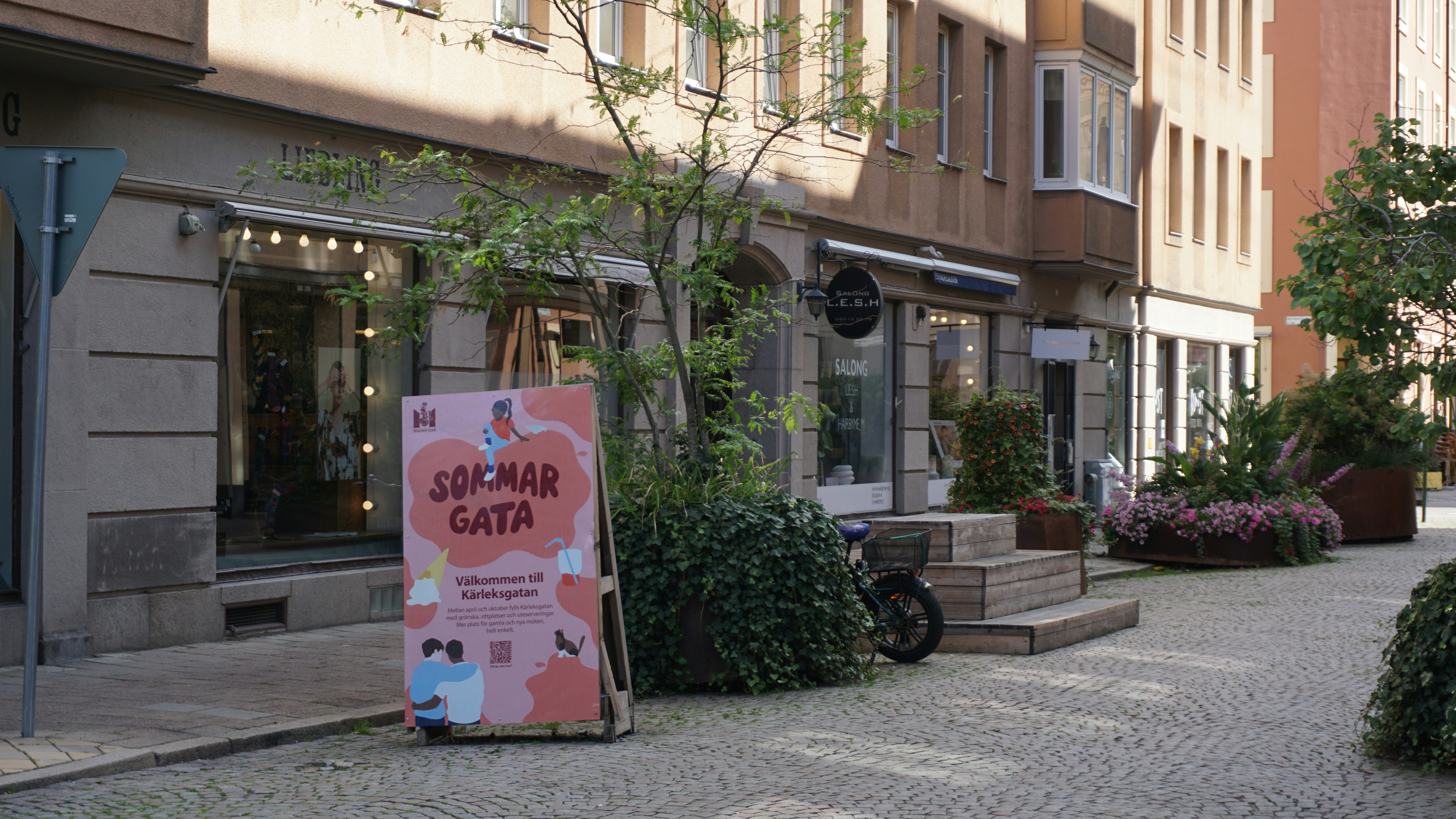 Pink signboard and quaint storefronts line a sunlit cobblestone street