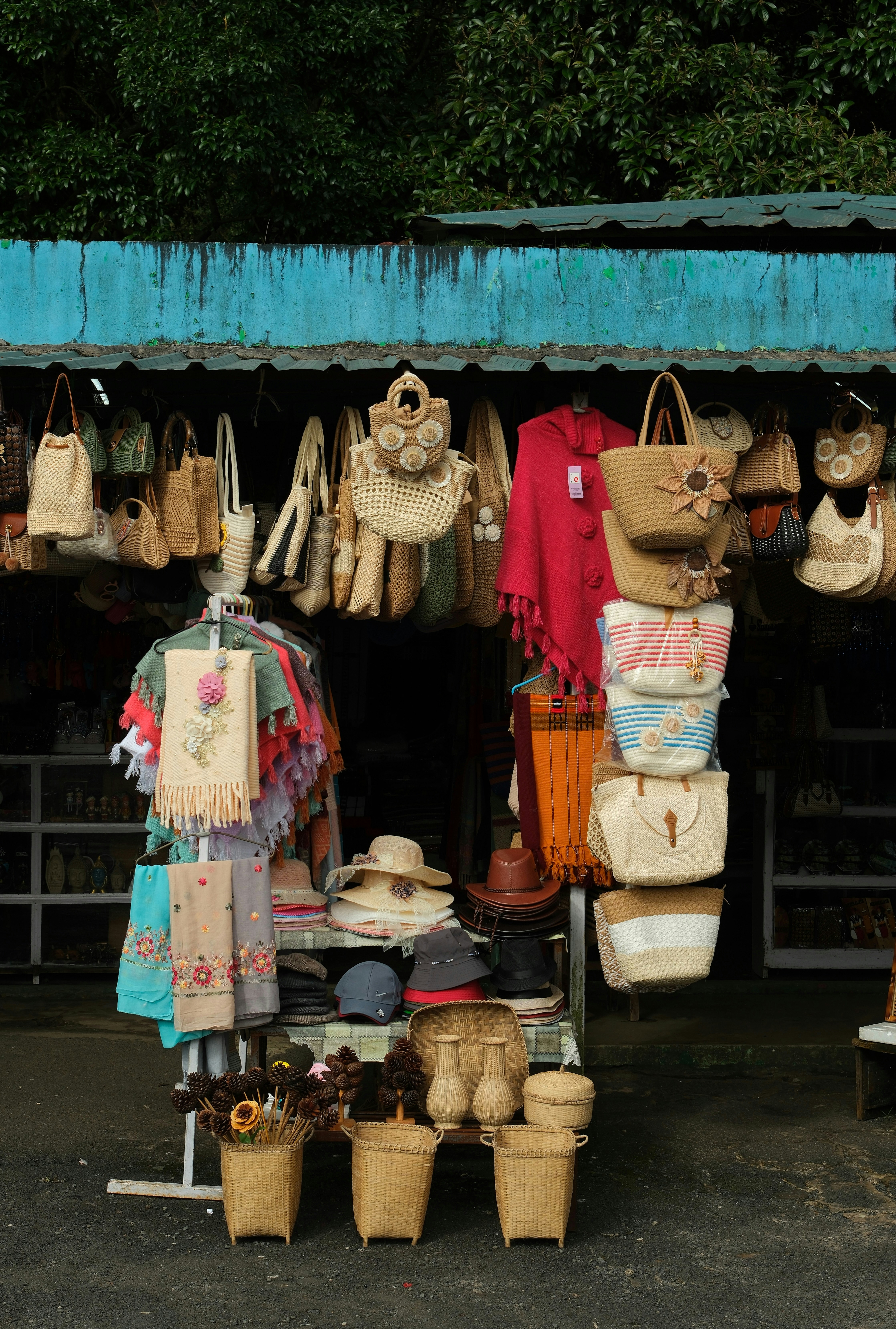 Vibrant storefront of woven hats, bags, and textiles arranged in a market stall, with bright turquoise trim and layered textiles creating a lively, organized clutter of handmade goods.