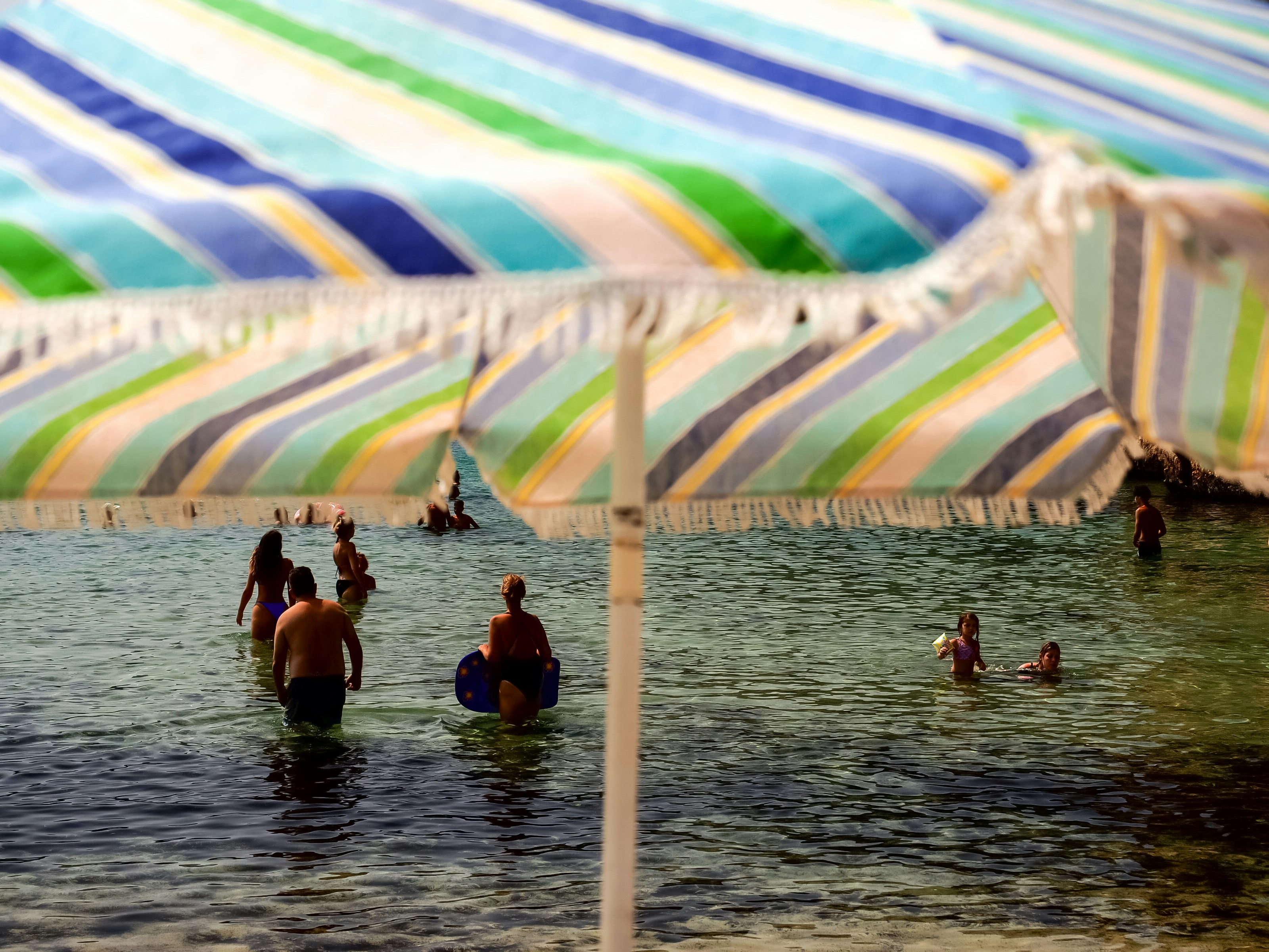 Stripe-shadowed Sea: Beachgoers Under a Colorful Canopy