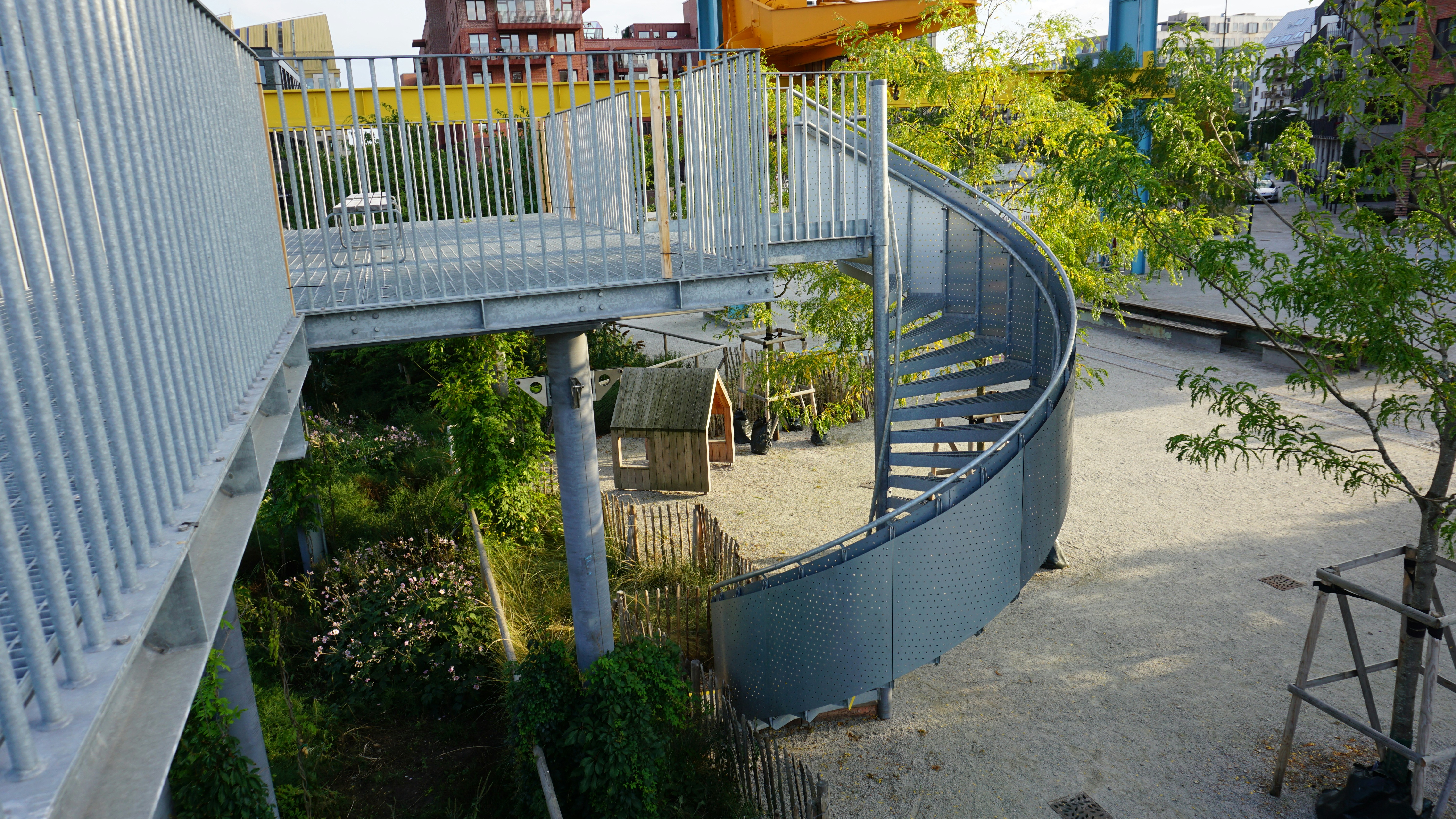 A metal spiral staircase descending from an elevated walkway into a park