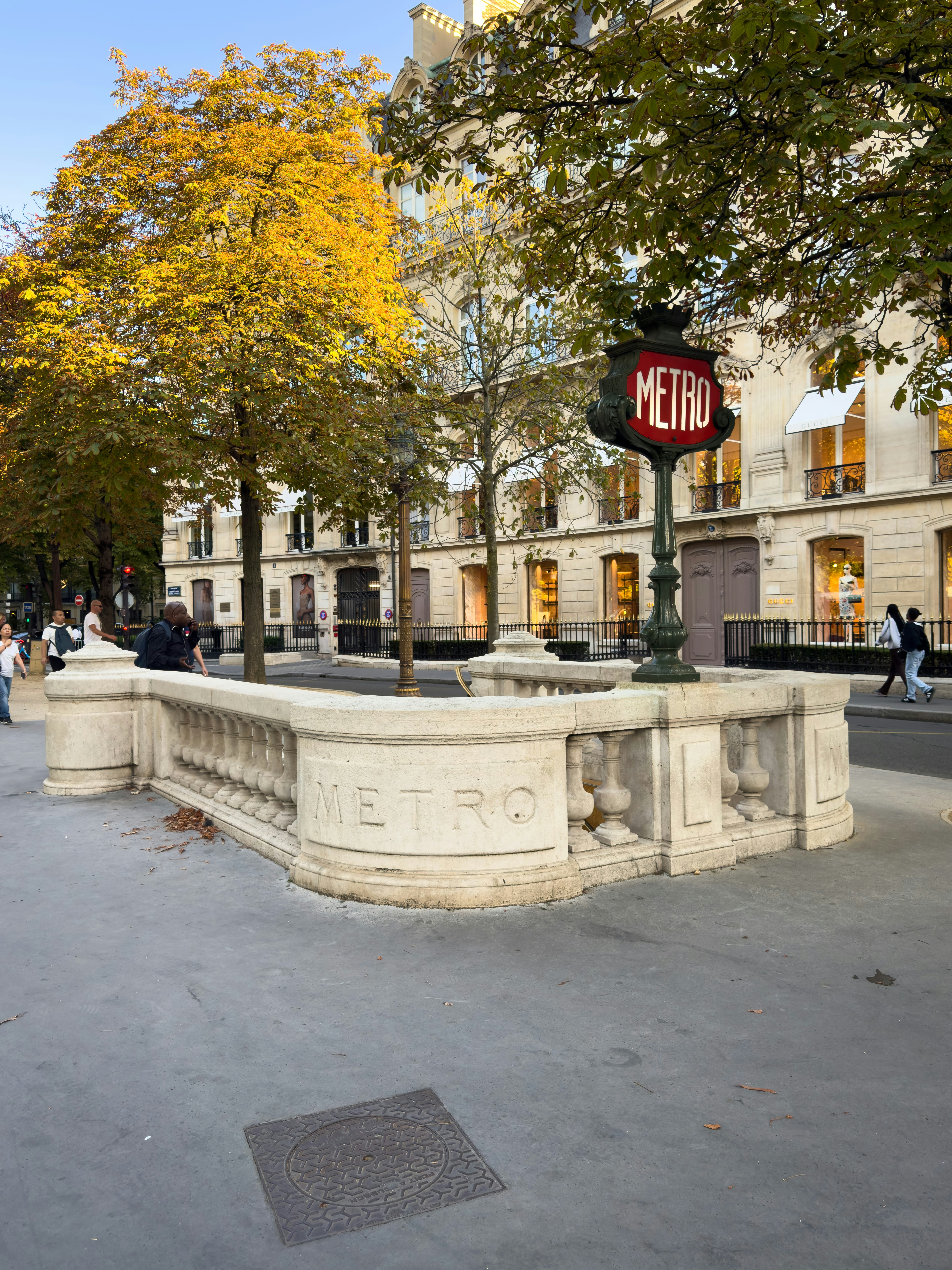 Metro entrance with classic signage and warm autumn trees in front of a stately Parisian building.