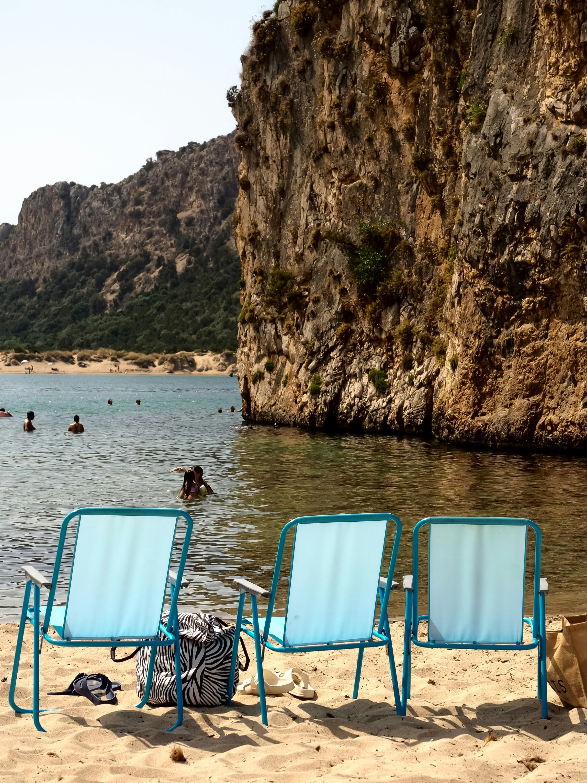 Blue Chairs on Sunlit Beach by a Rugged Cliff