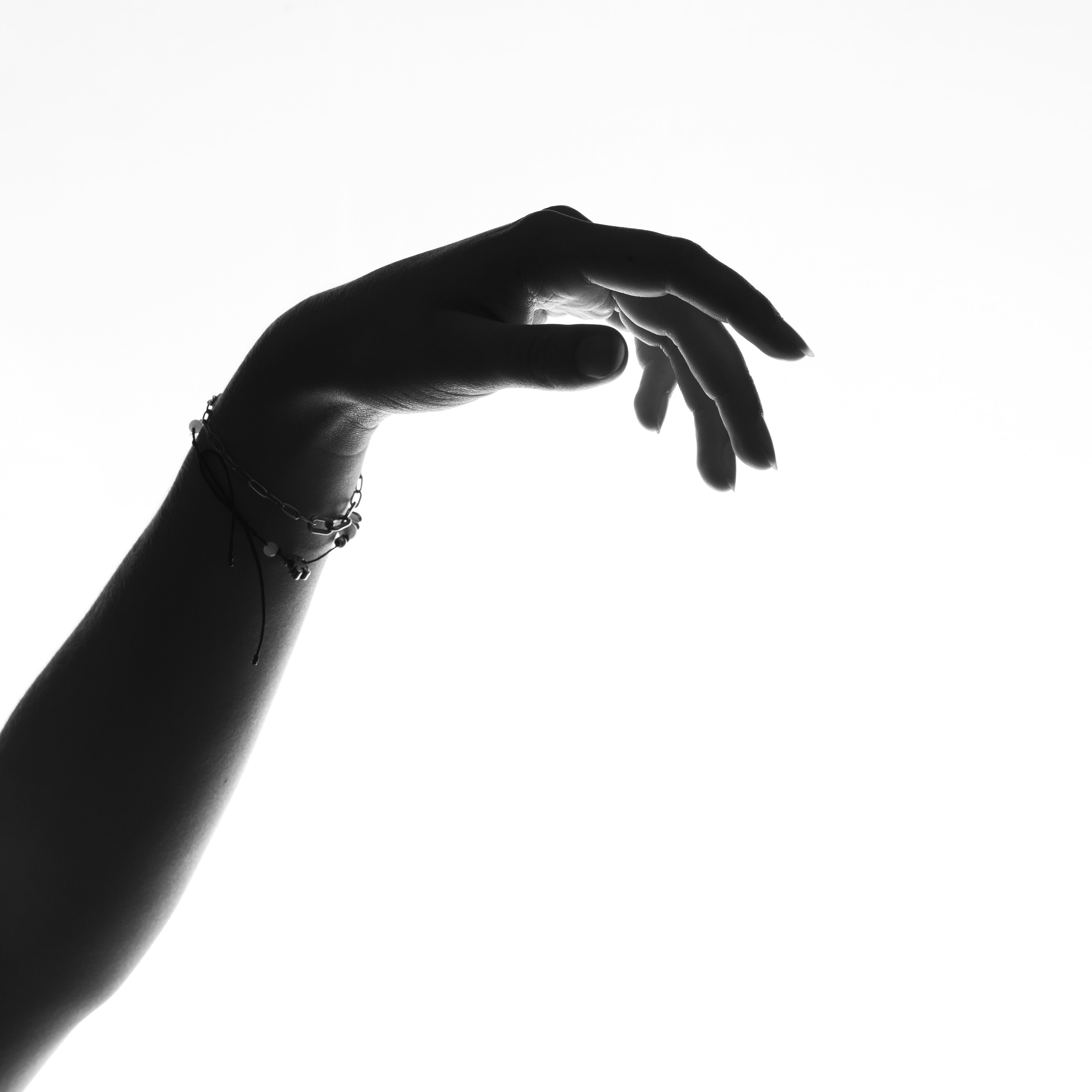 A stark silhouetted forearm and hand against a bright background, highlighting delicate contours and bracelets. The image emphasizes negative space and the graceful arc of the fingers.