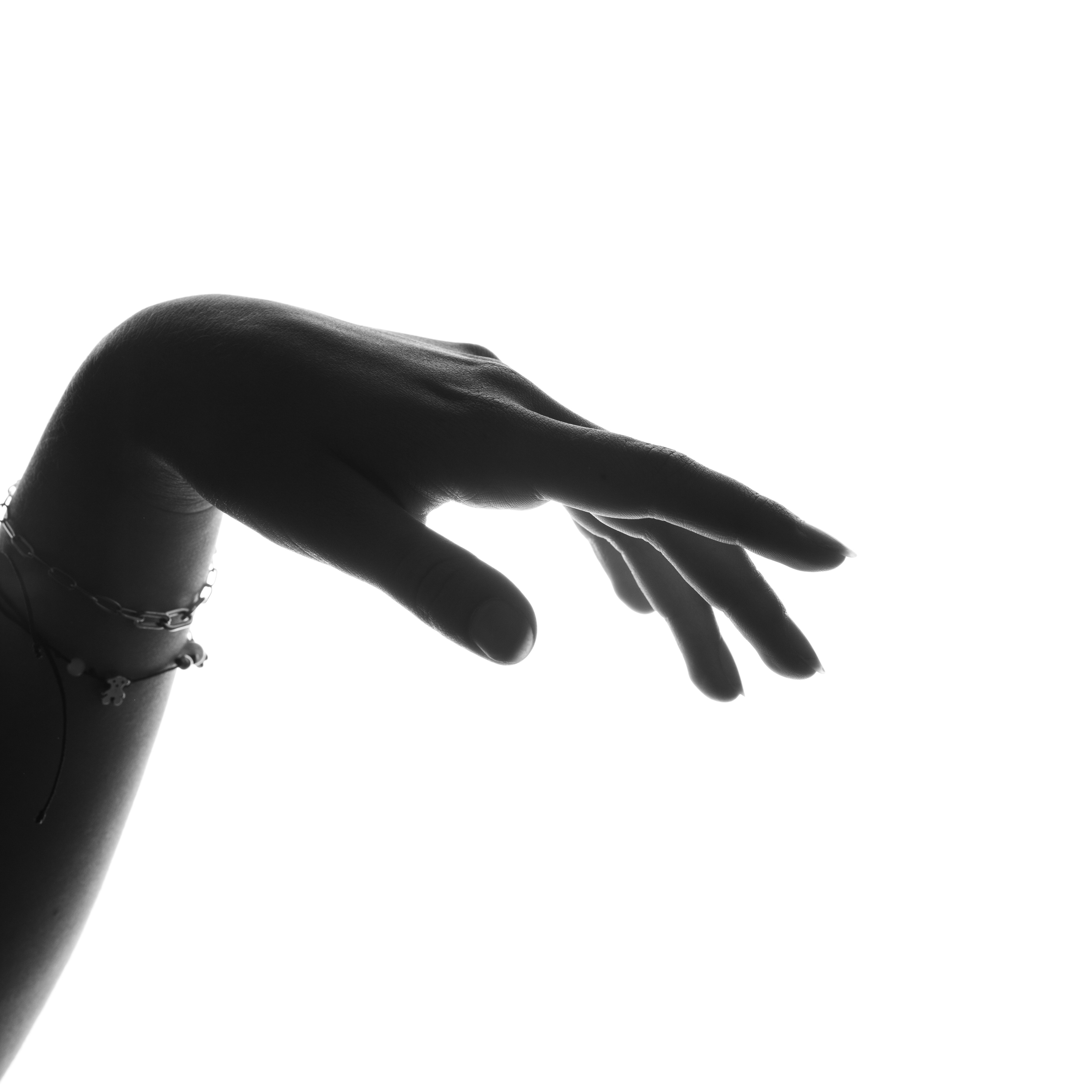 A solitary, backlit silhouette of a hand and forearm with bracelets, set against a pure white background, conveying simplicity and grace without visible facial features.