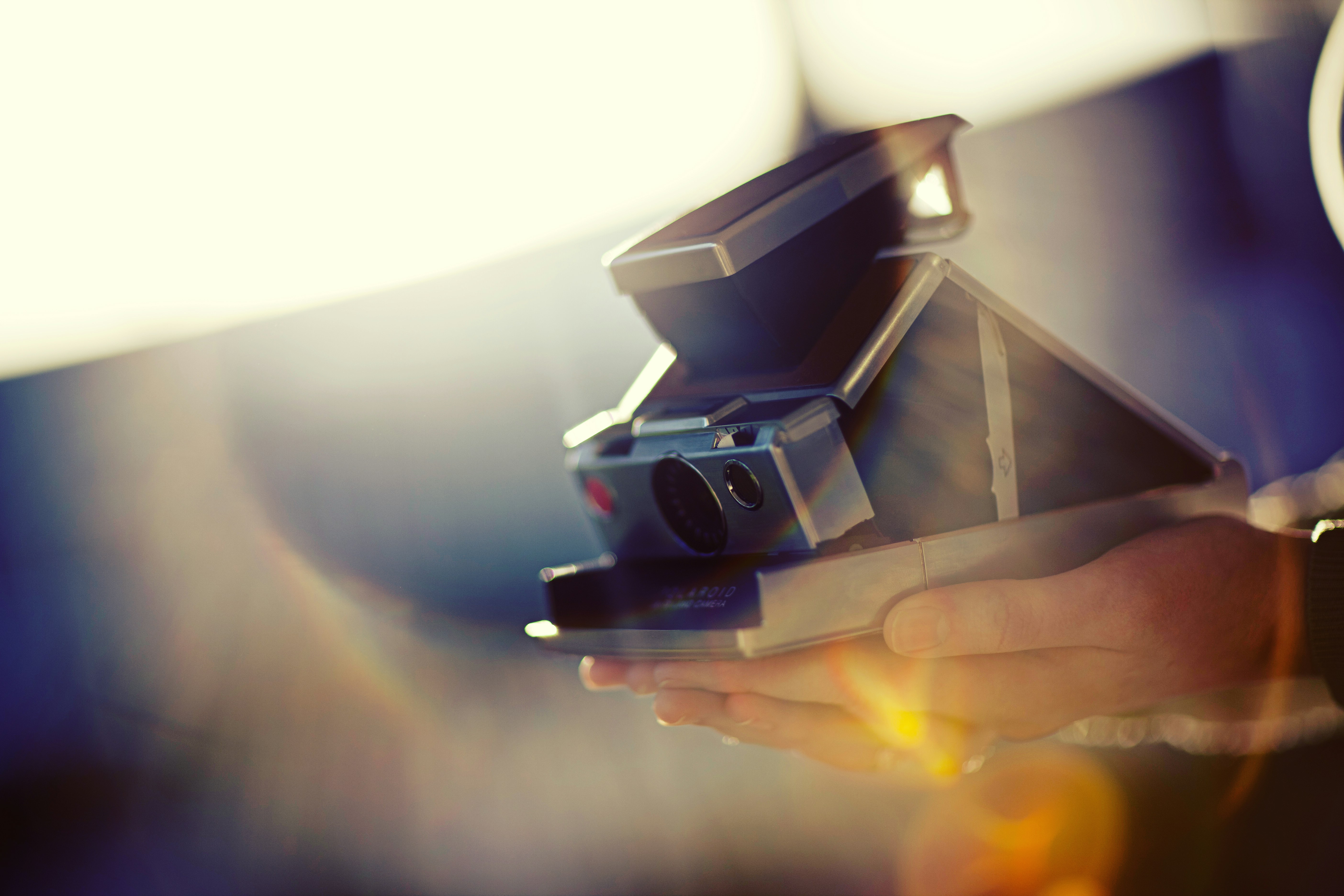 A person holding a vintage instant camera in bright backlit golden light