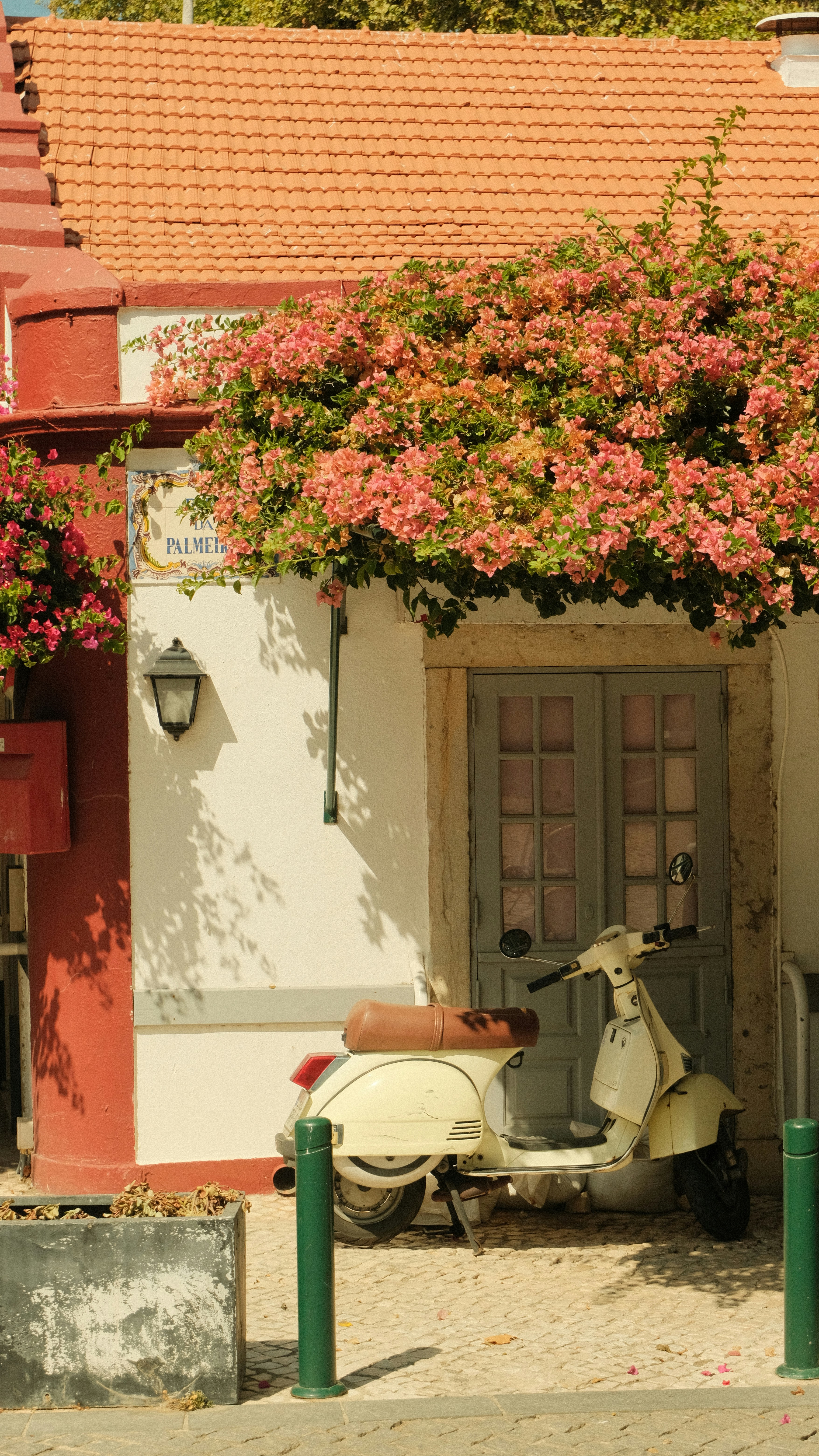 A cream scooter parked before a doorway with pink bougainvillea under a tiled roof