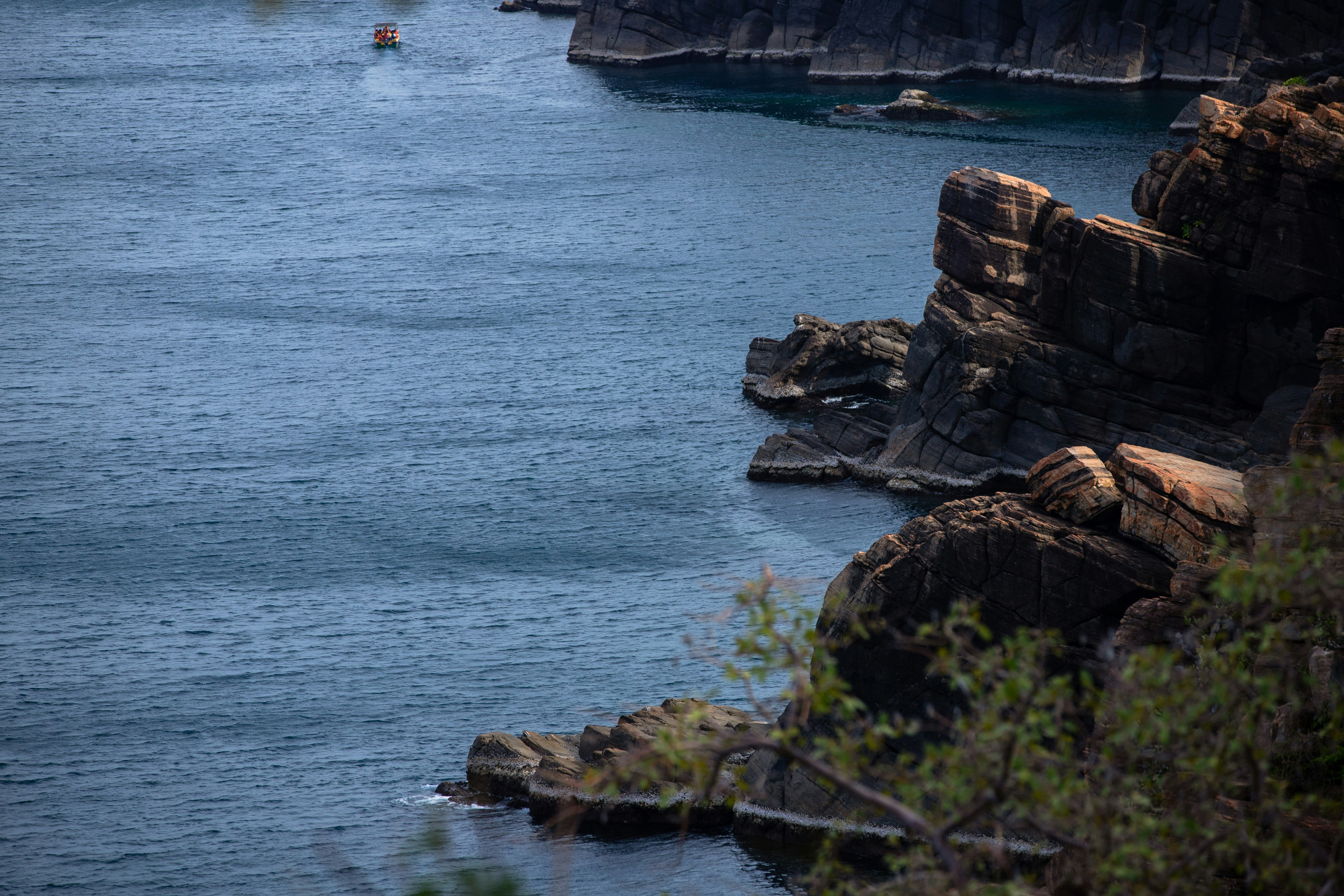 Coastline with blue water and rugged rocky outcrop along the shore; a small portion of foreground foliage hints at depth. A minimal landscape scene suitable for tranquil coastal imagery.