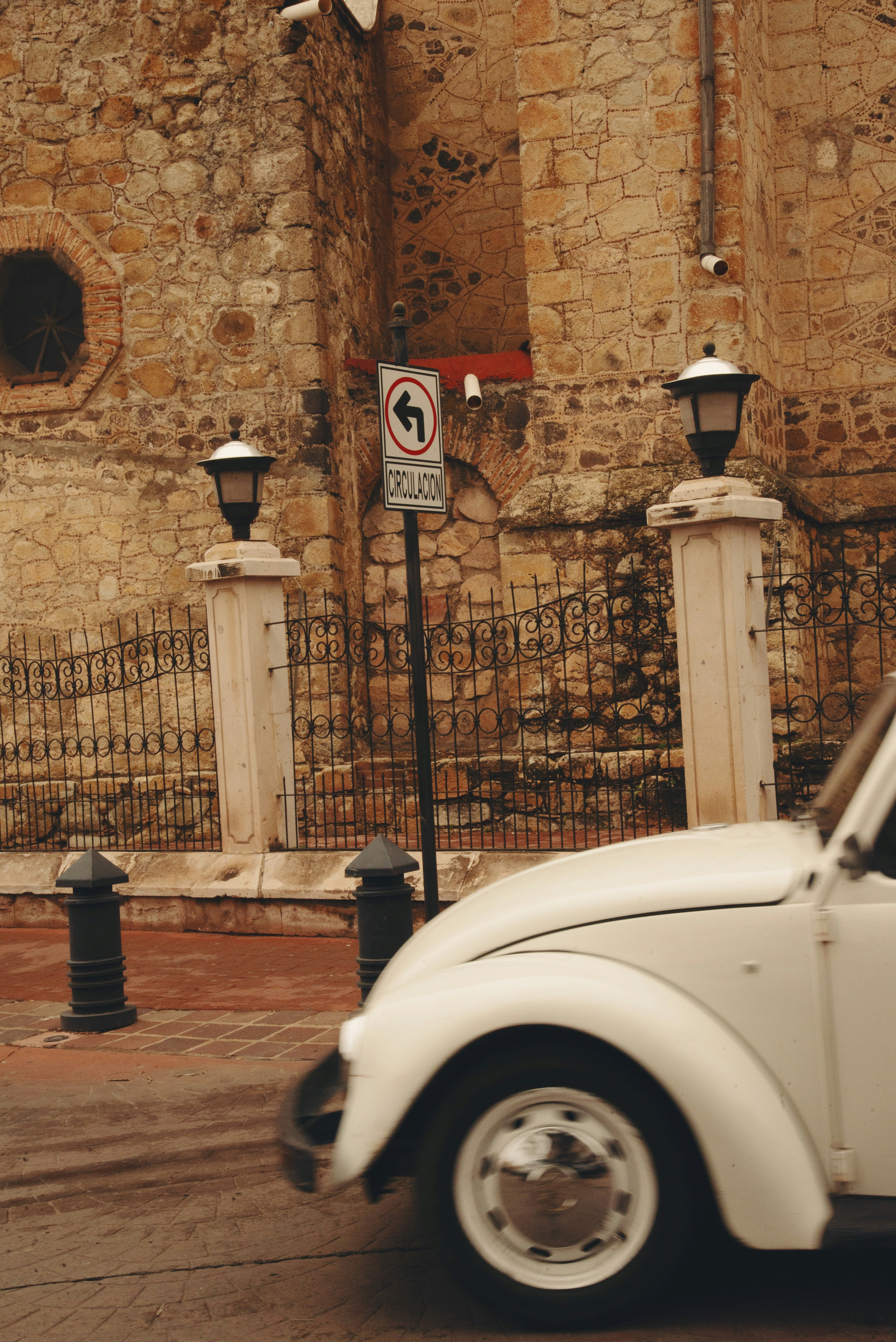 White vintage car and stone gatehouse along a sunlit street