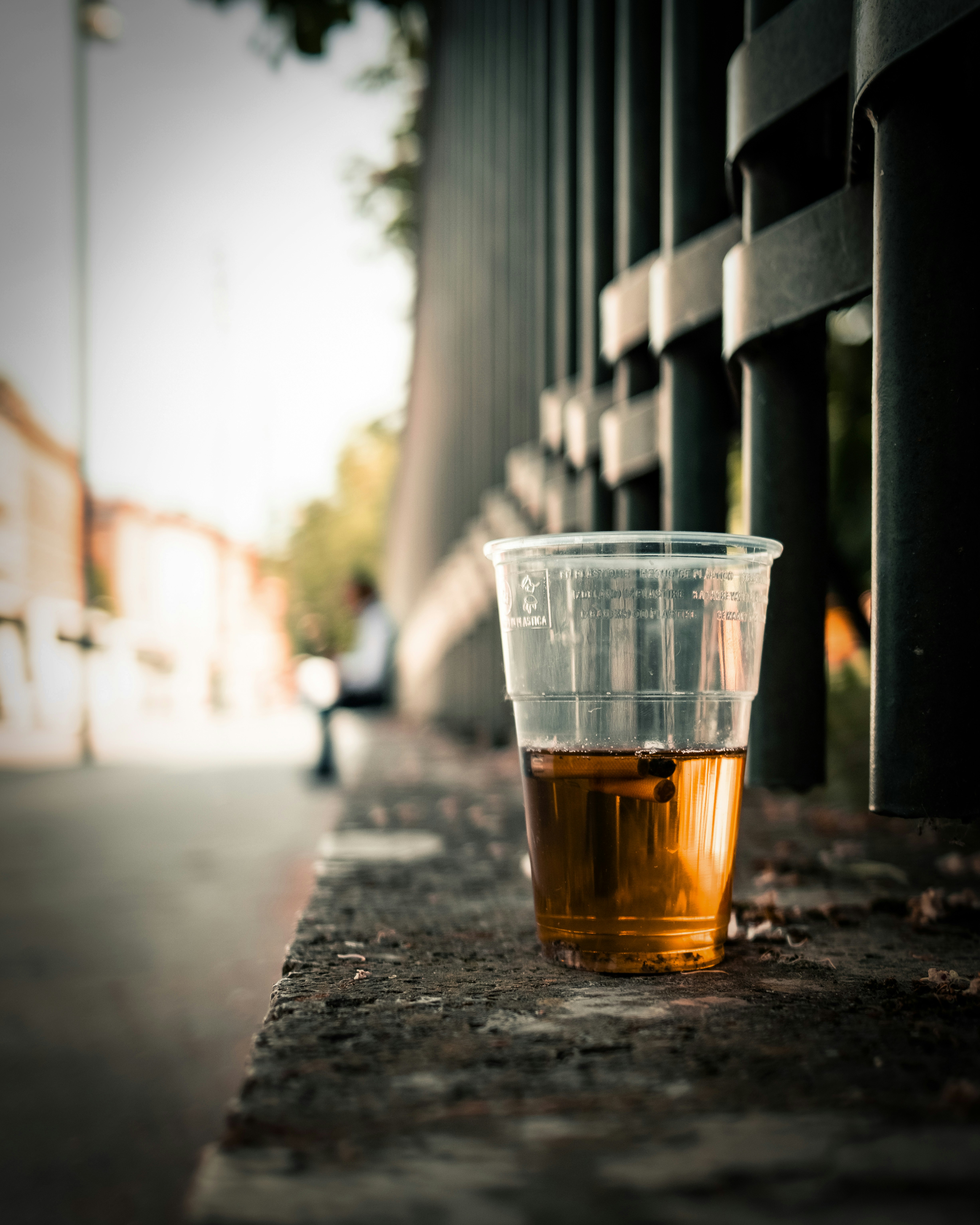 Amber Cup on the City Curb: A Quiet Moment by the Fence
