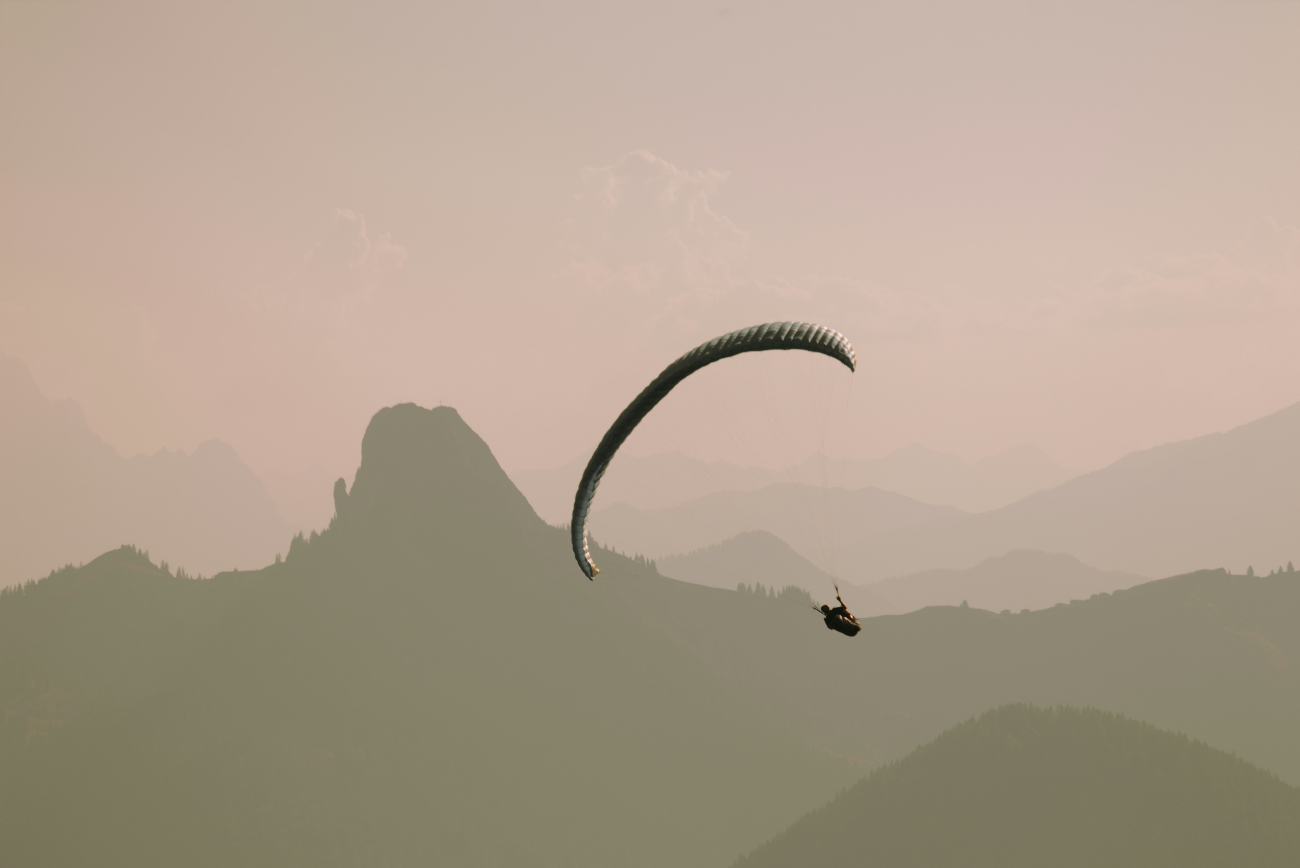 Graceful arc: a lone paraglider against a layered mountain horizon