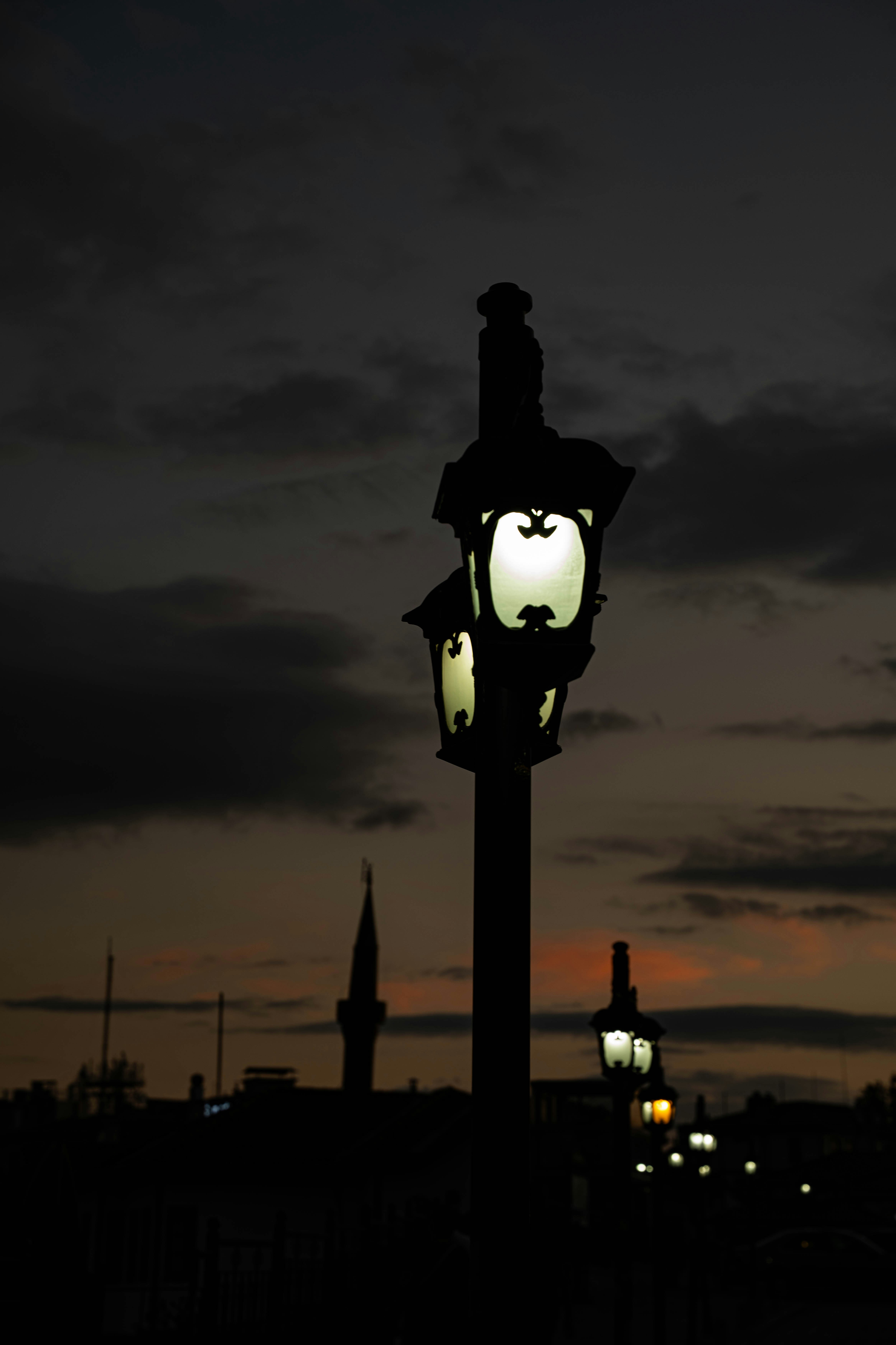 Lit street lamps against a dark evening sky with a distant minaret silhouette