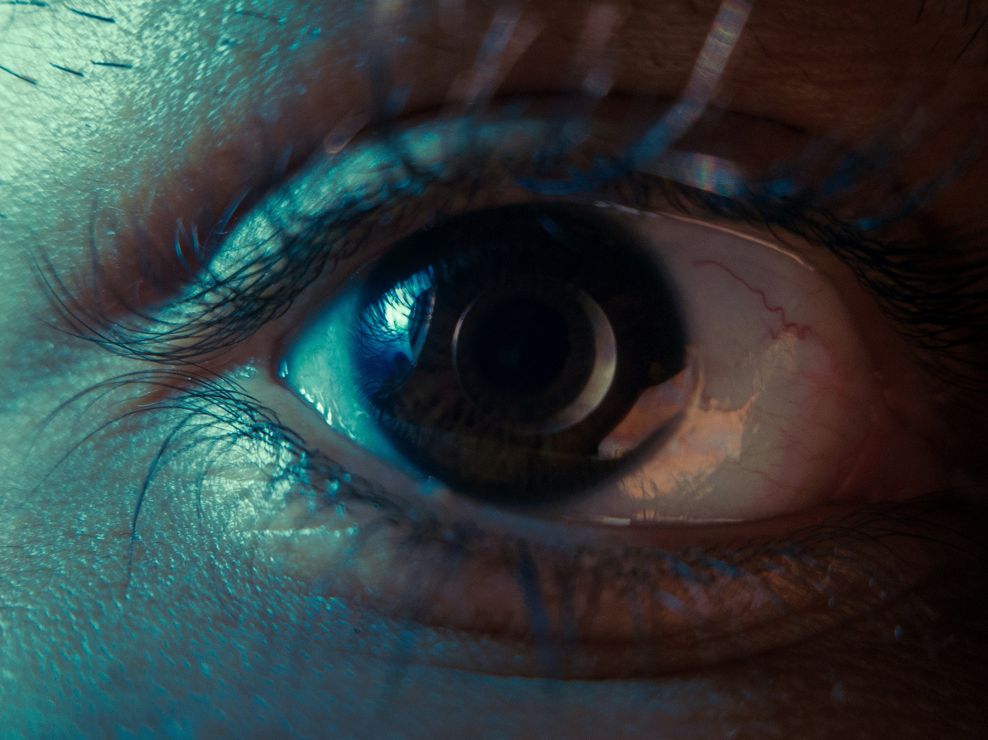 Close-up of a human eye with teal lighting and strong detail in the iris and lashes, emphasizing texture and moisture; a photographic study of ocular detail.