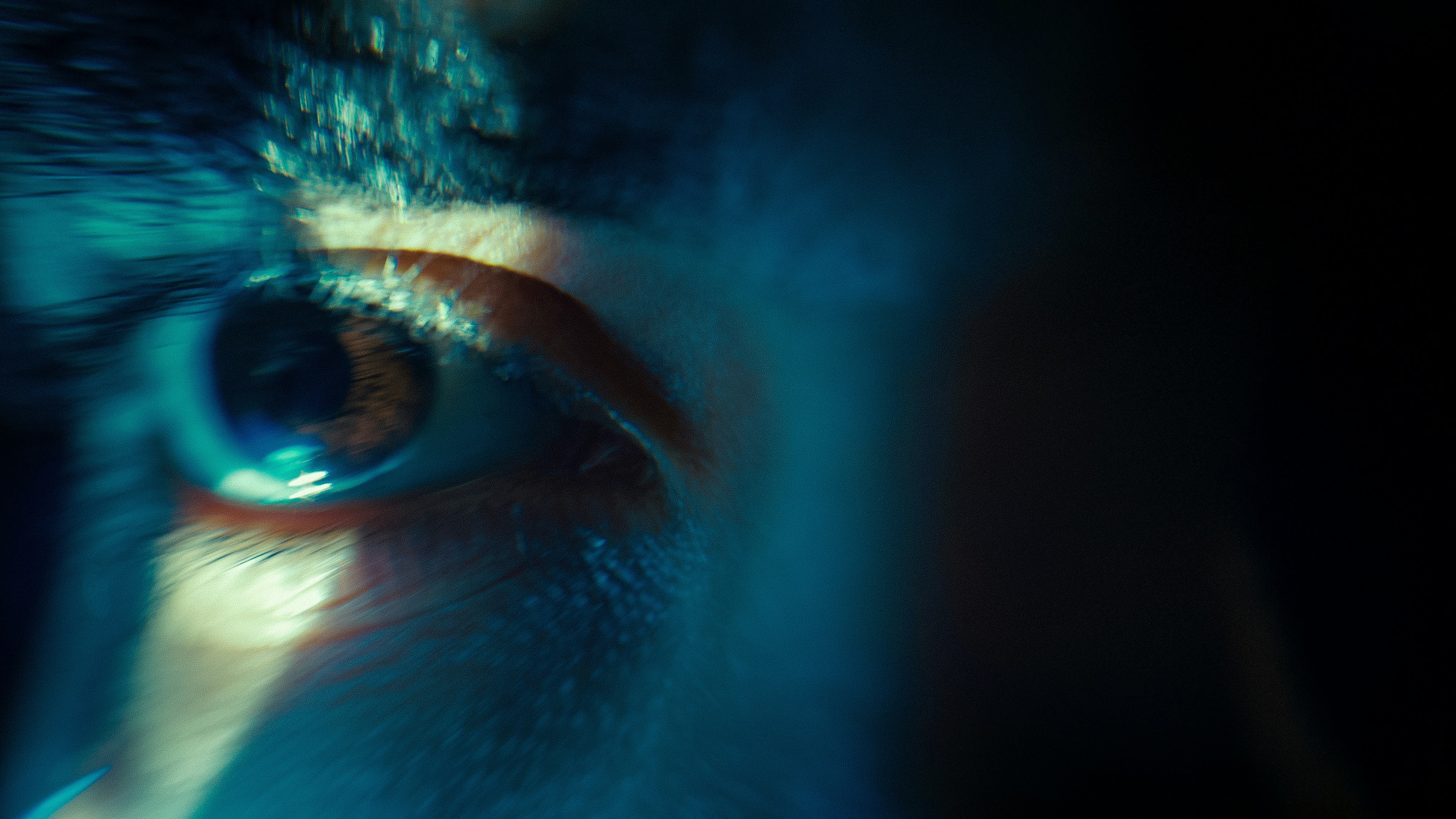 Close-up of a human eye bathed in blue light with moisture on the skin, emphasizing a dramatic, moody atmosphere.