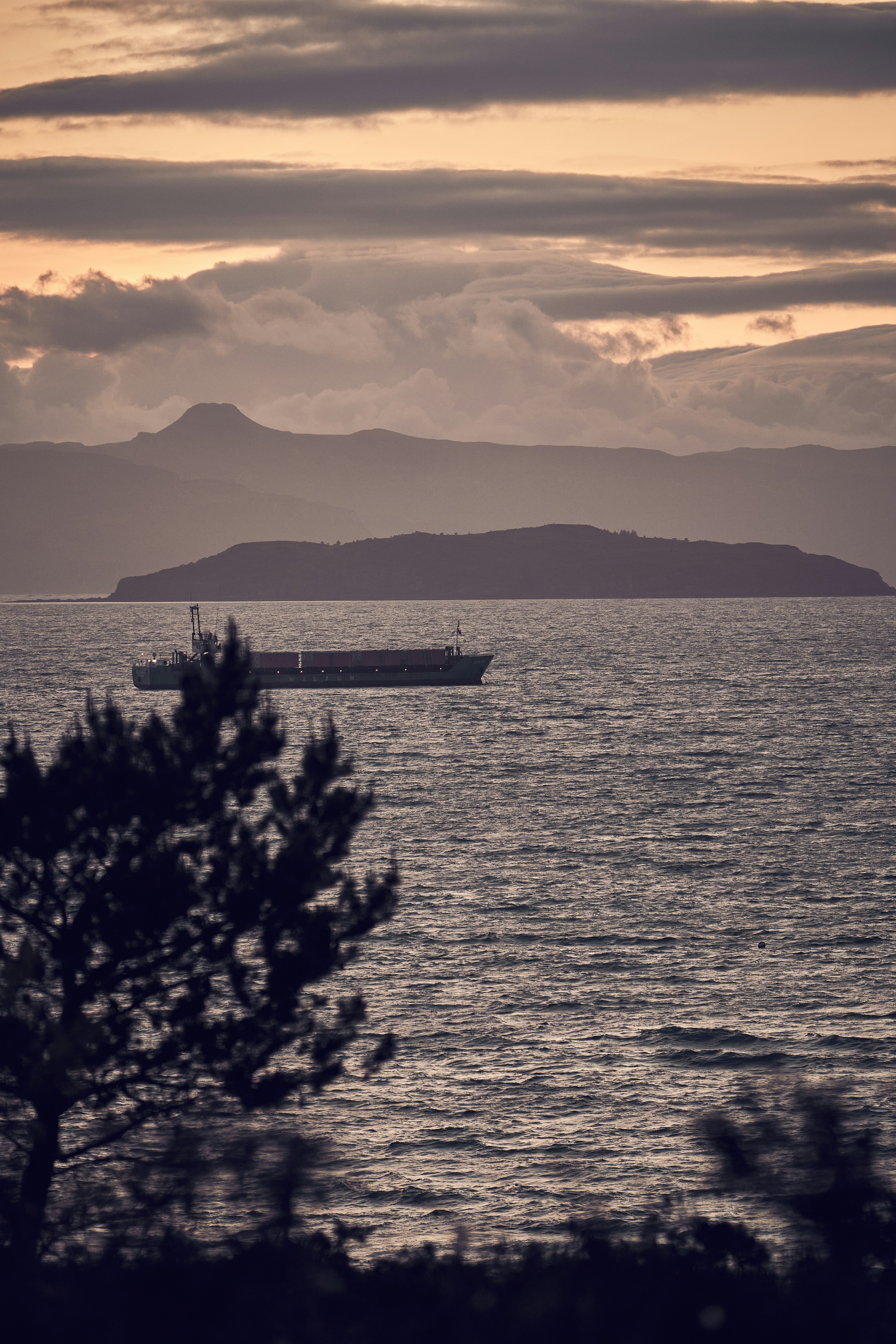 Silhouette of a distant ship crossing a tranquil sea at dusk