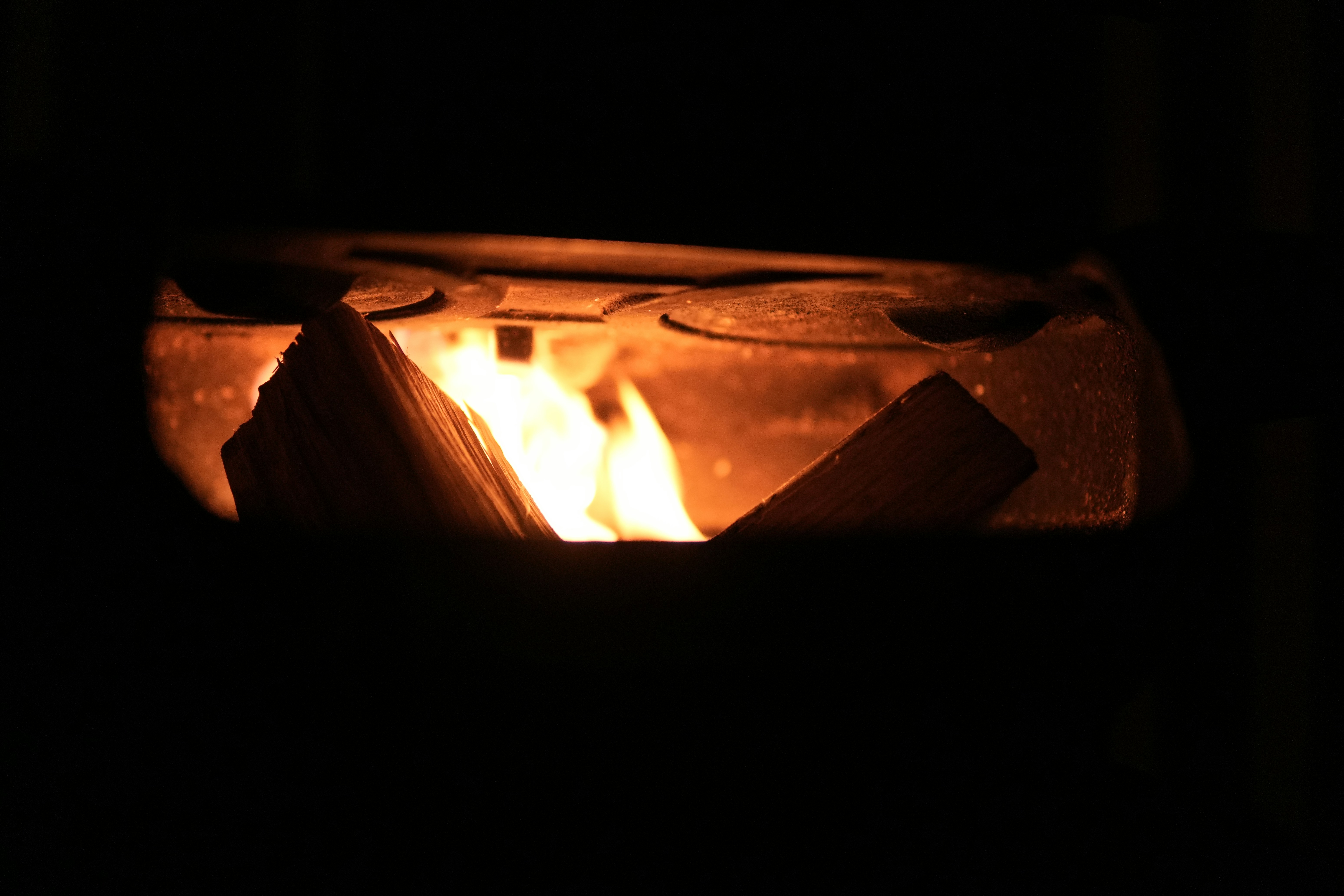 Bright orange flames burning between two pieces of wood inside a dark stove