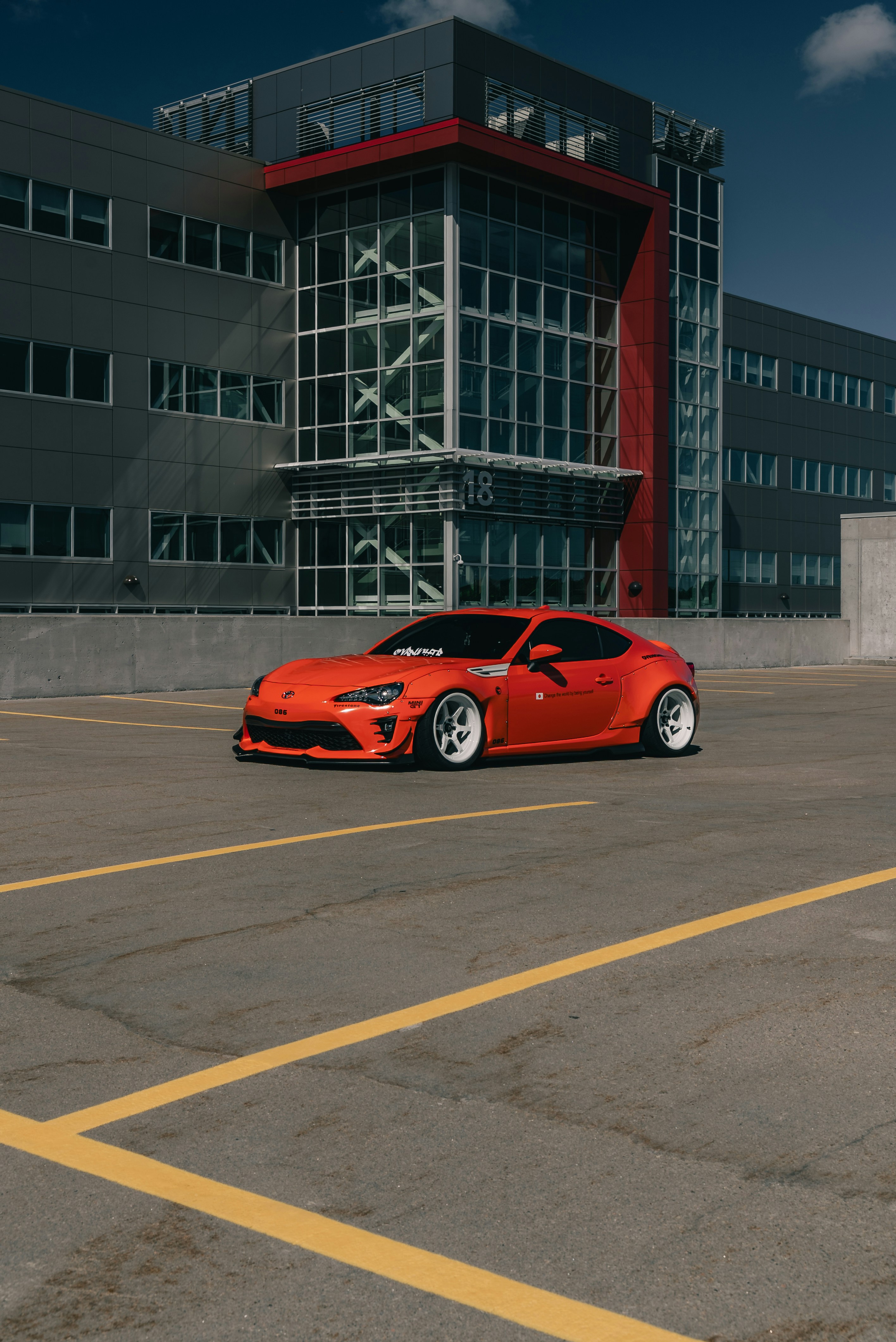 Red sports coupe anchors a modern campus plaza beneath glass and steel