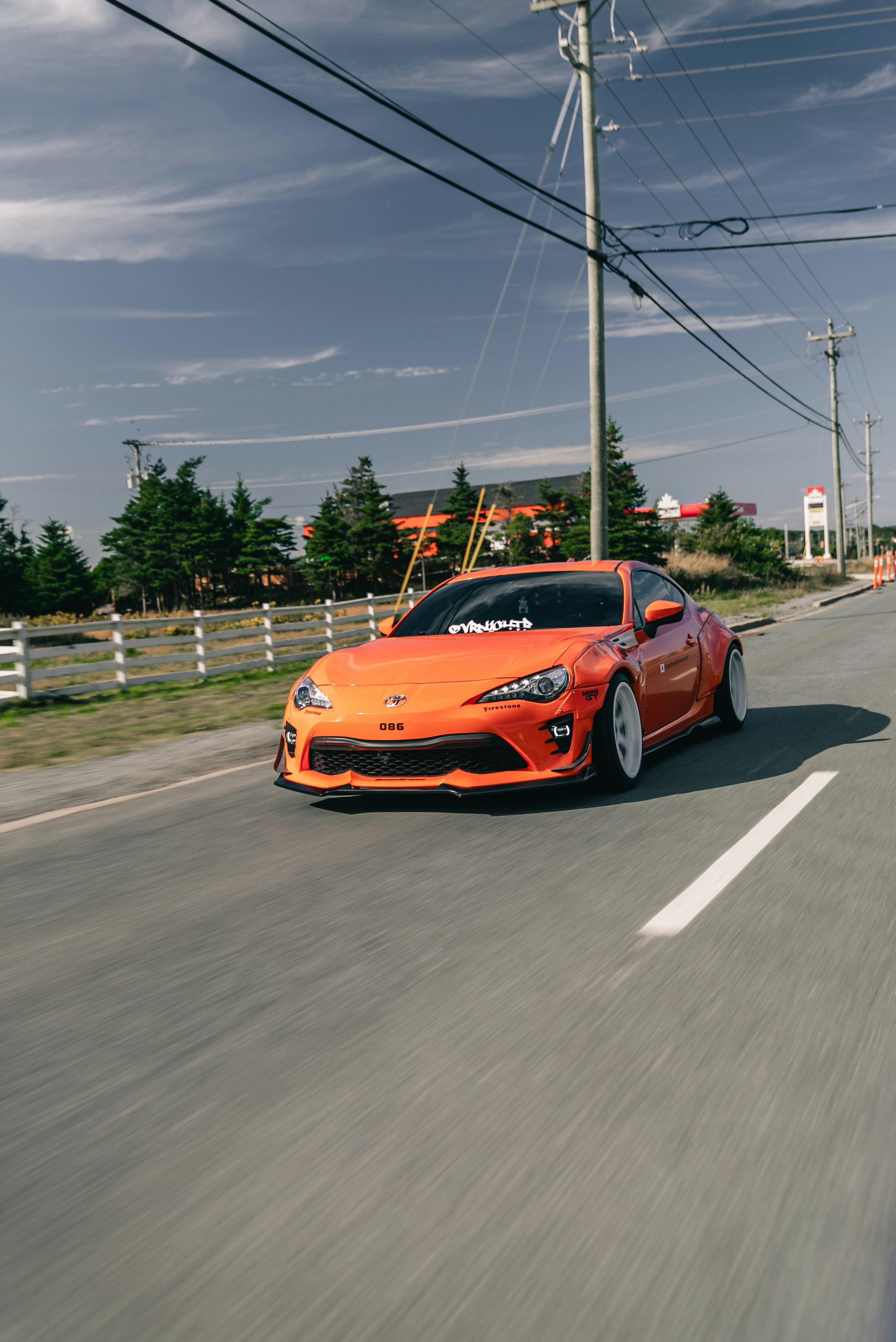 Orange sports car prowling a sunlit suburban road