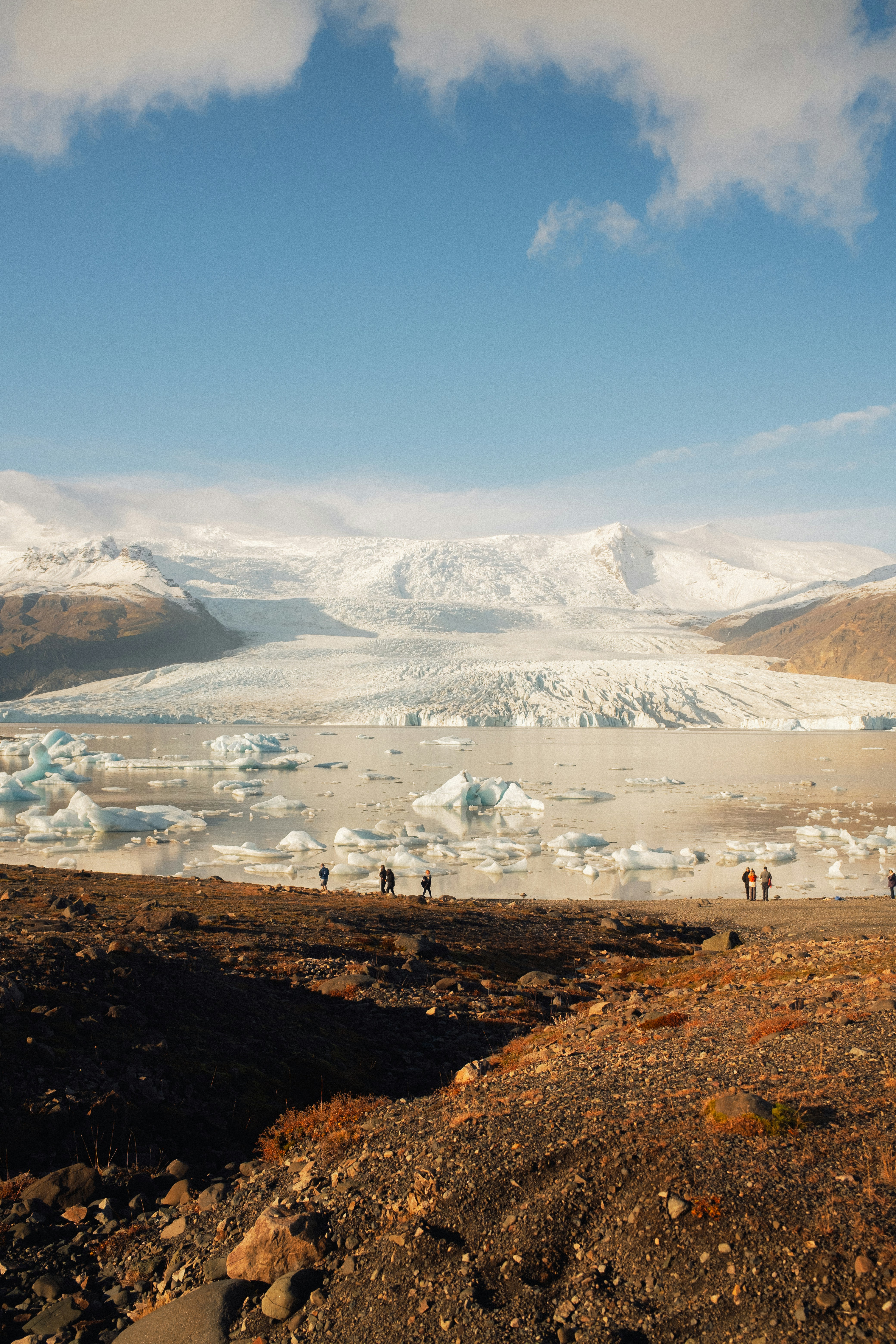 Glacial Reach: Trekker Silhouettes at a Polar Lake