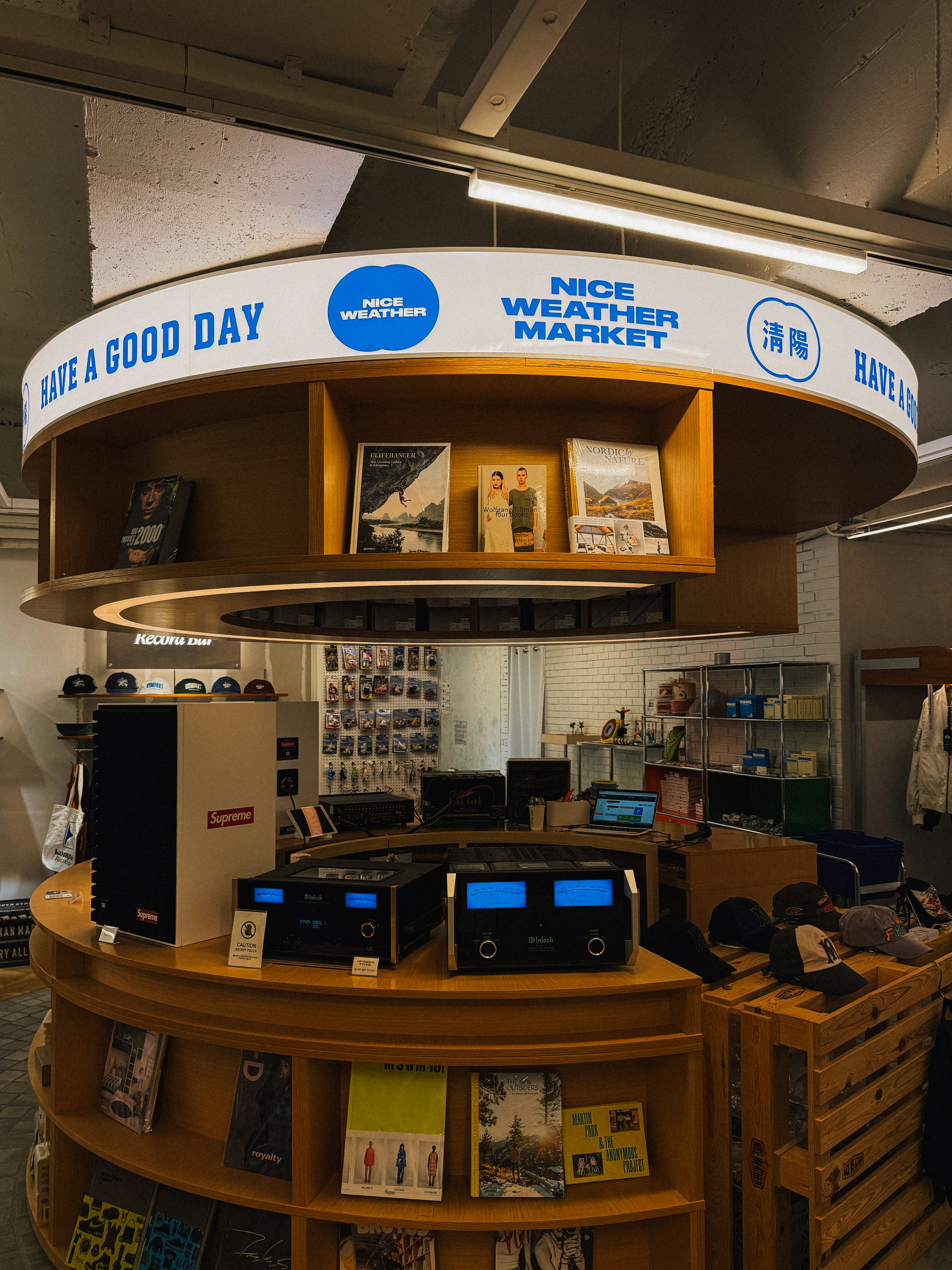 A circular information desk within a market setup featuring shelves, framed photos, and electronic kiosks. The scene includes a bright white circular sign overhead with blue branding and a warm wood-toned counter.