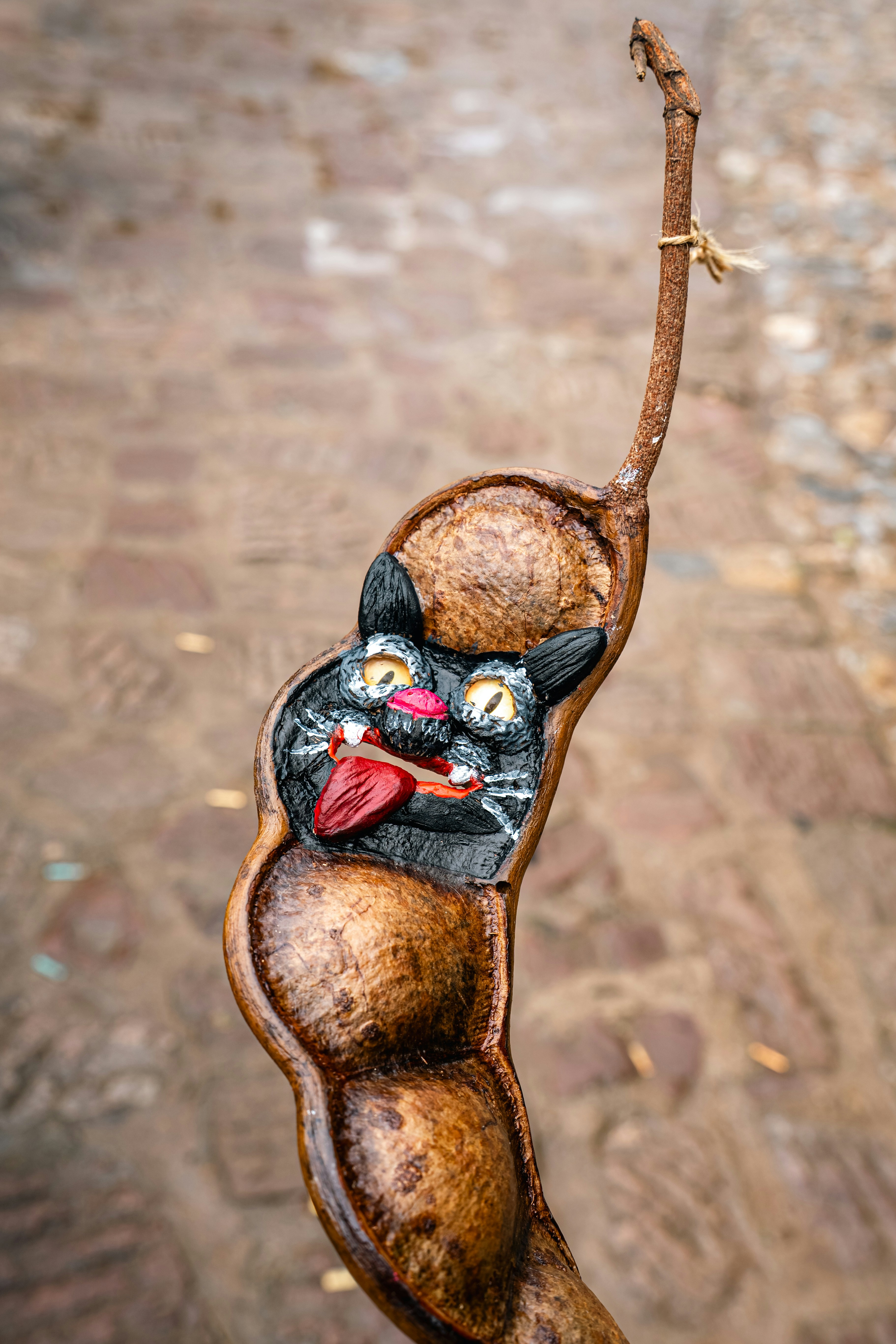 Grinning seed pod: a carved wooden cat monster on a rainy street