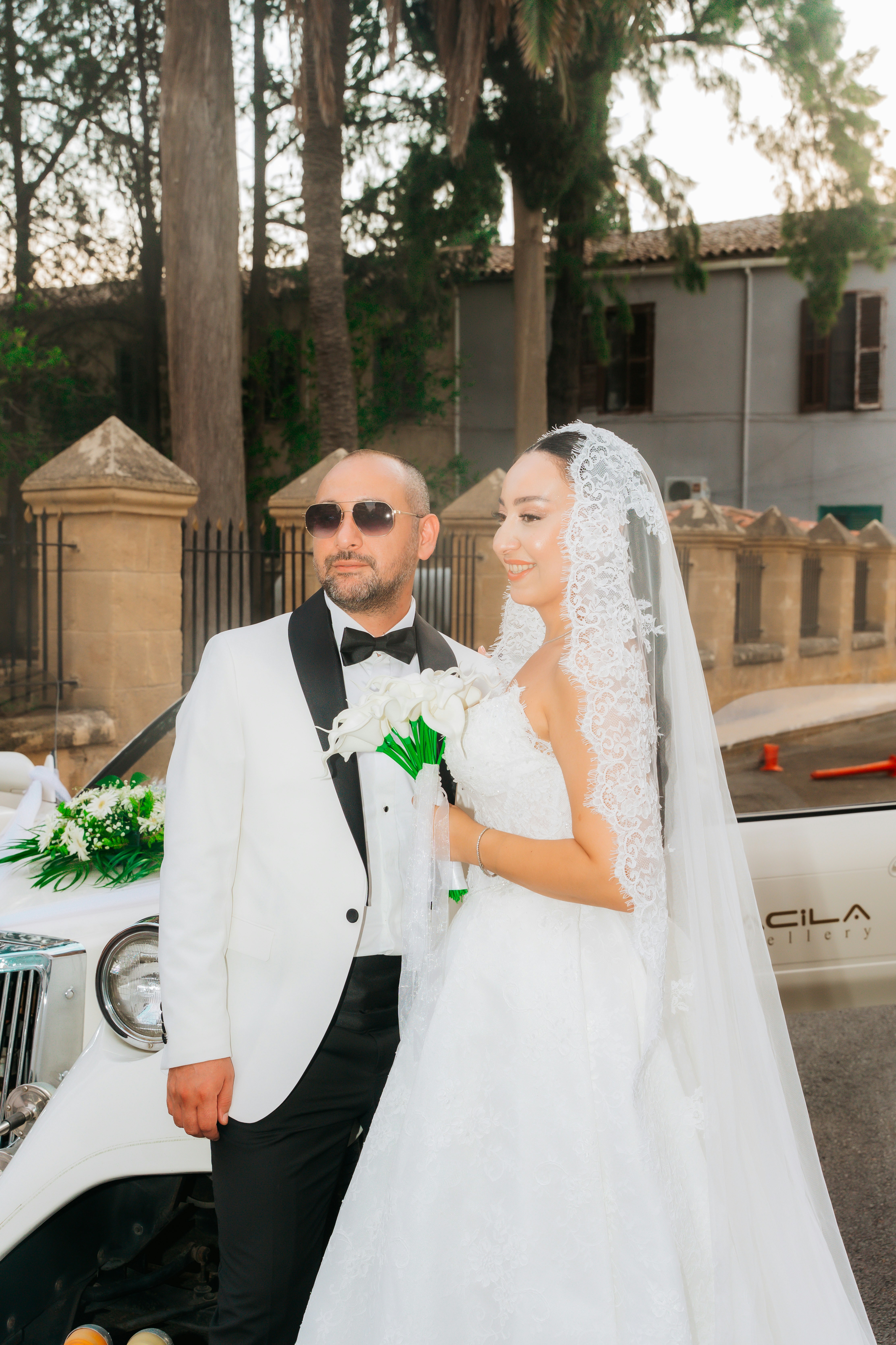 Bride and Groom in White: A Quiet Moment by the Classic Car