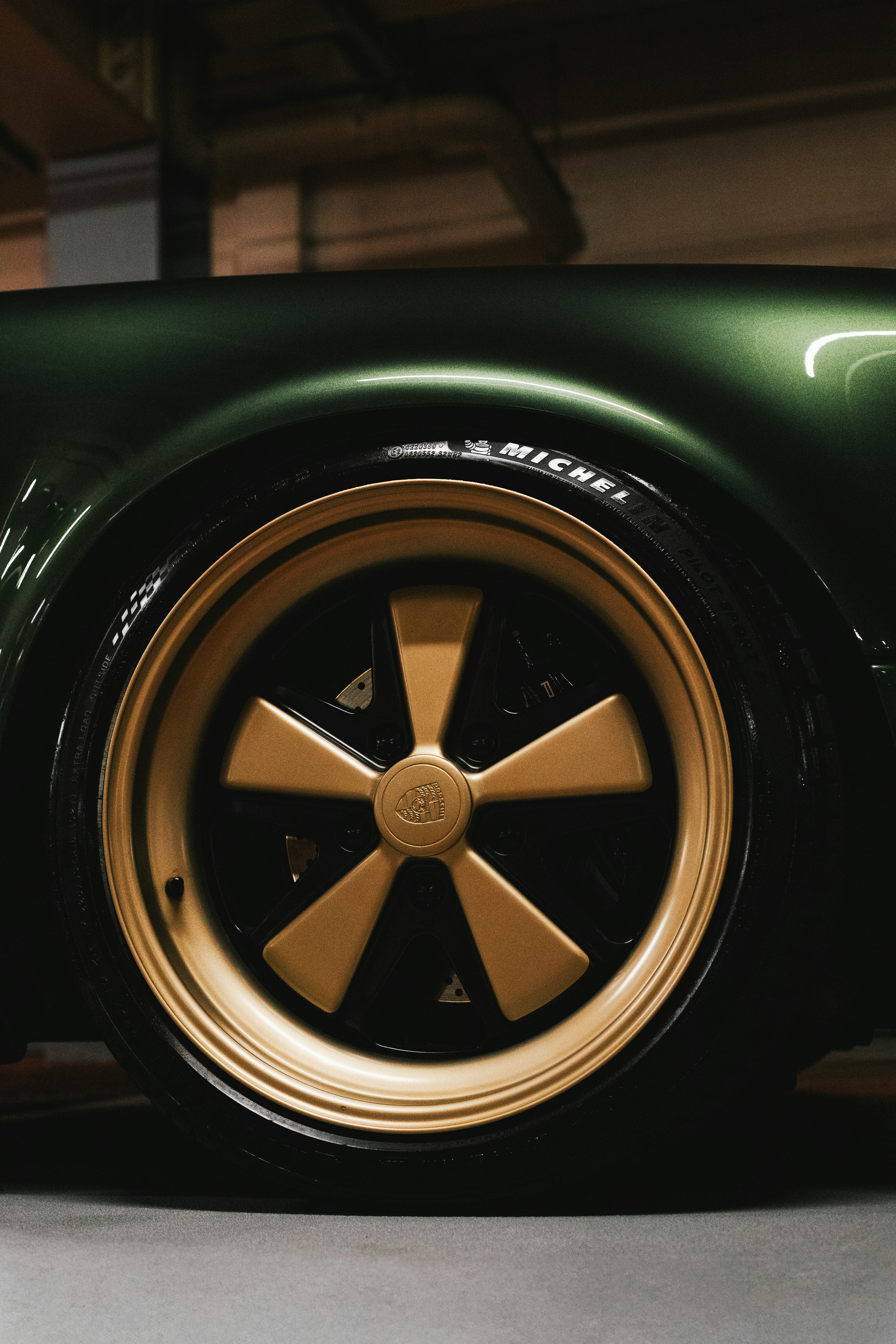 Gold-centered wheel of a vintage-green car peeking from the frame