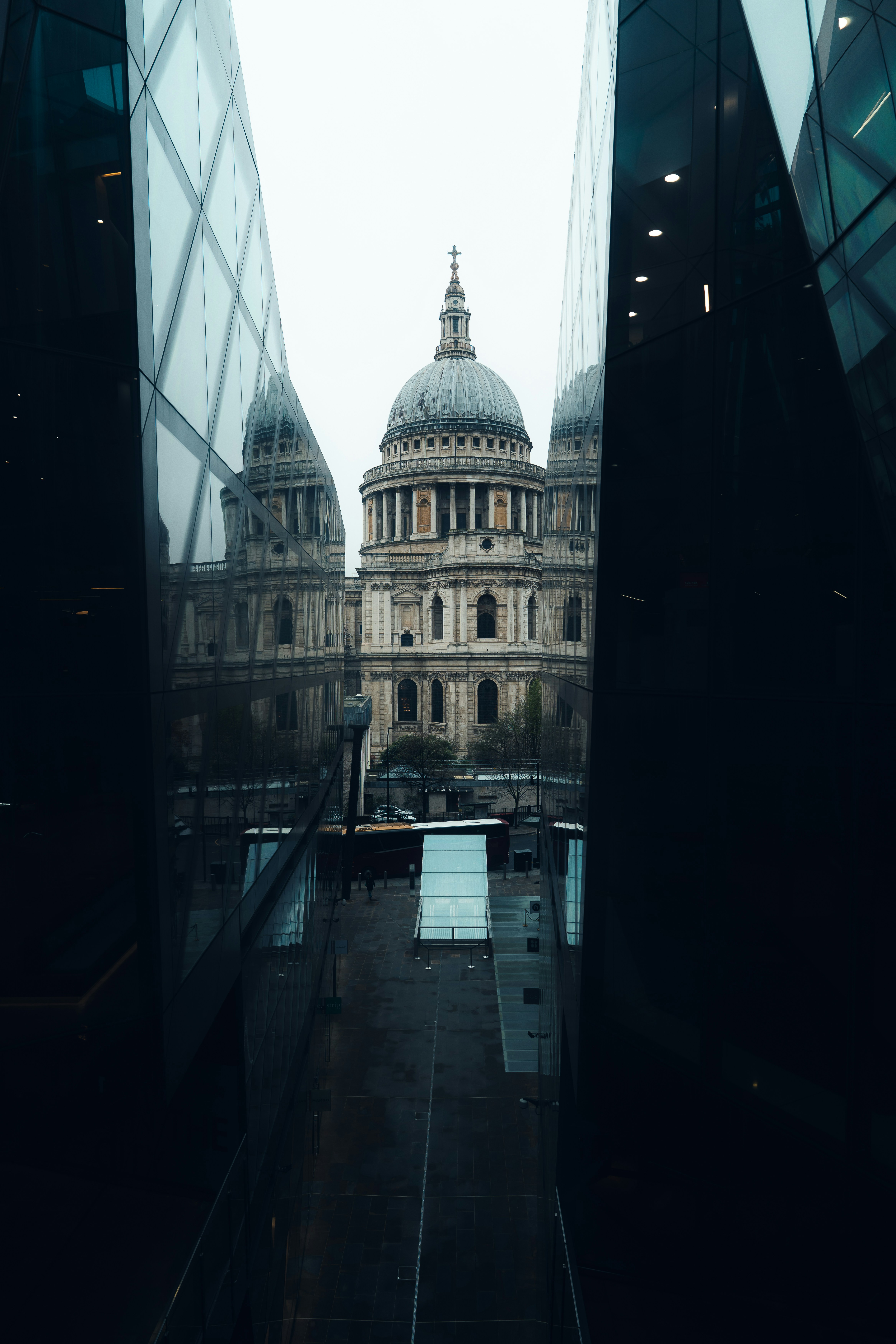 Stately cathedral framed by mirrored glass walls of a modern street, creating a dramatic corridor toward the dome. A contrast between historic architecture and contemporary reflections.