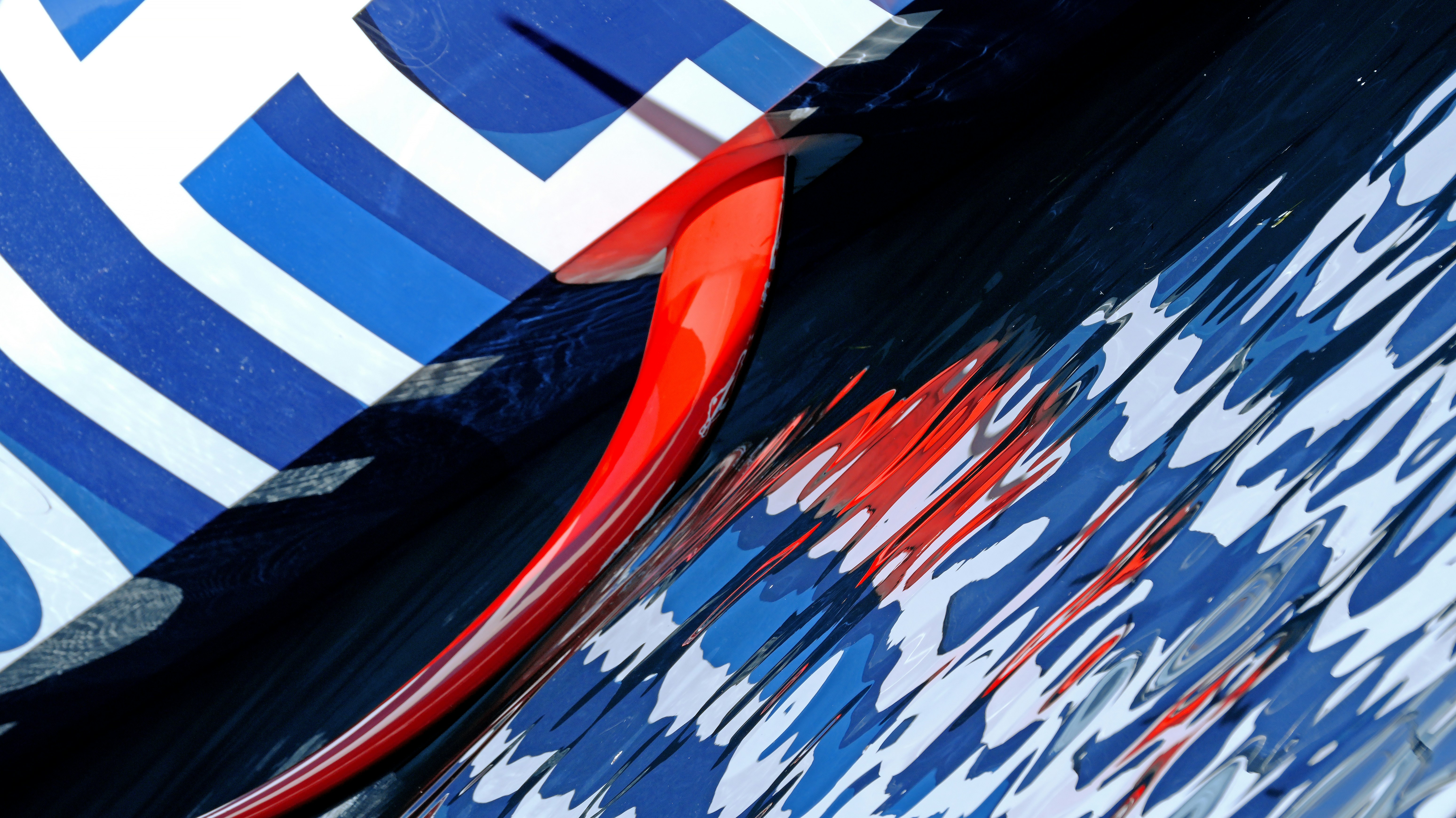 Bleached ripples and a red arc: a close-up of abstract boat curving through reflected stripes