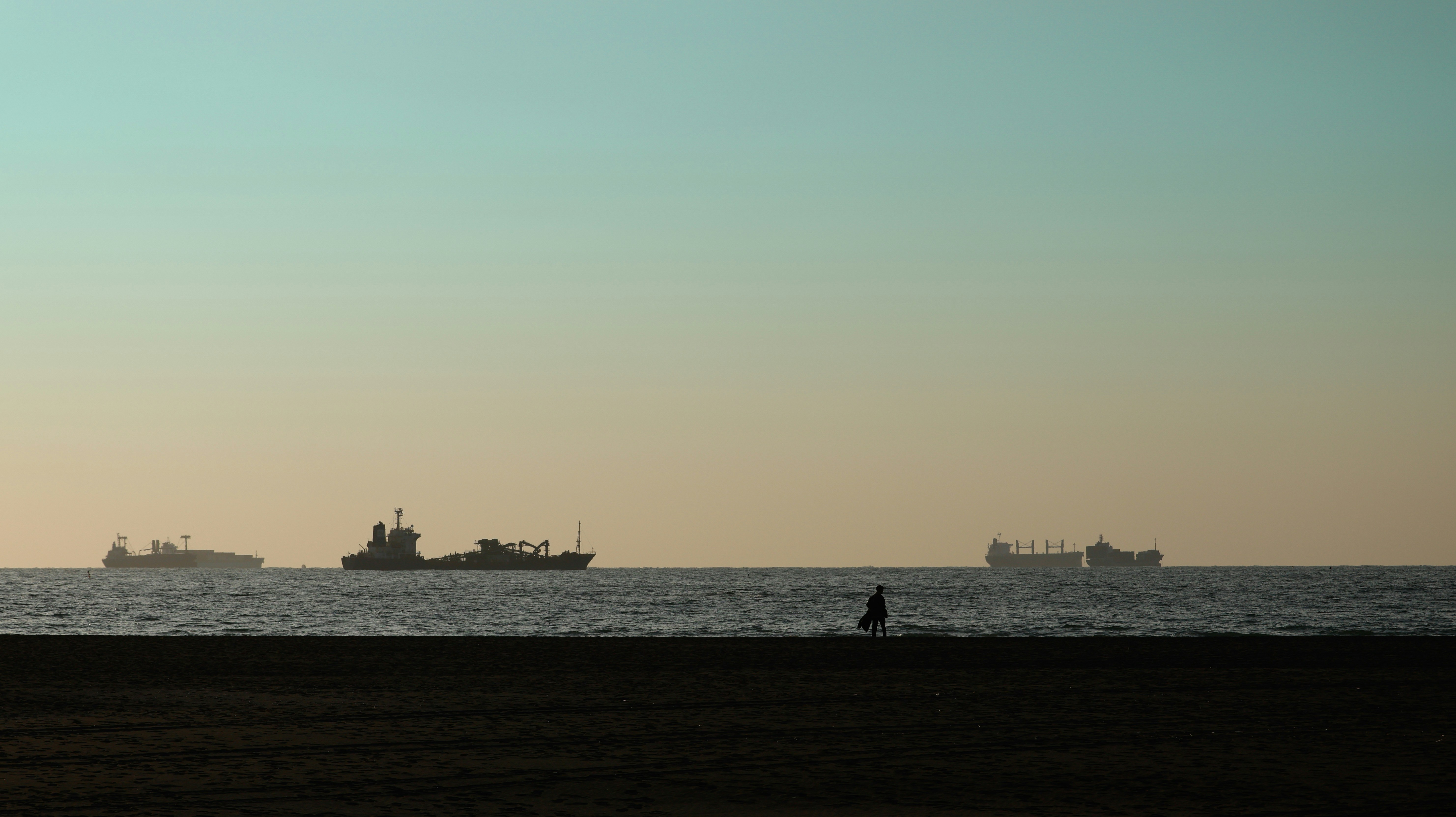 Silhouetted shoreline: ships on a calm horizon at dusk