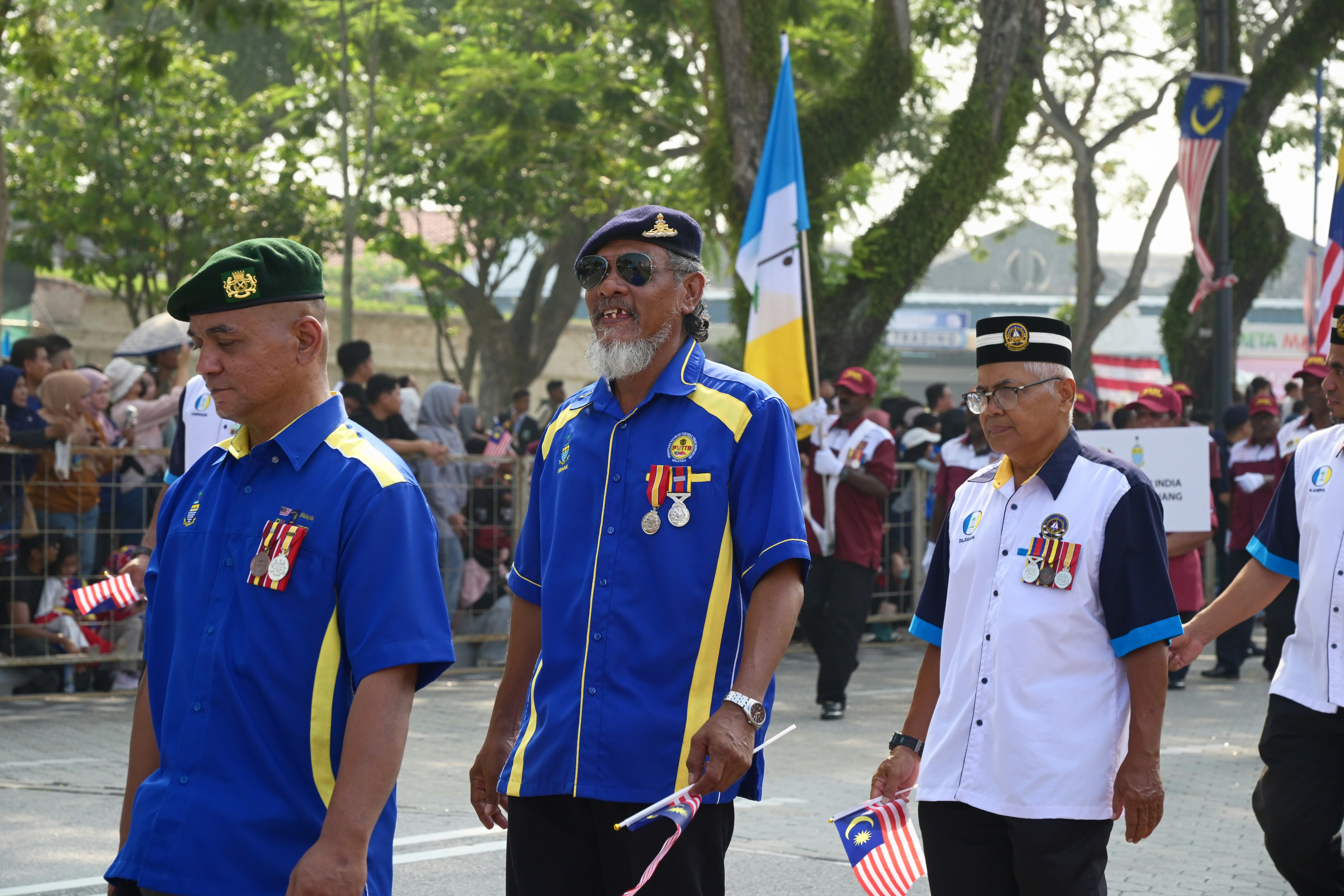 A community delegation in blue uniforms carries Malaysian flags through the Merdeka parade.
