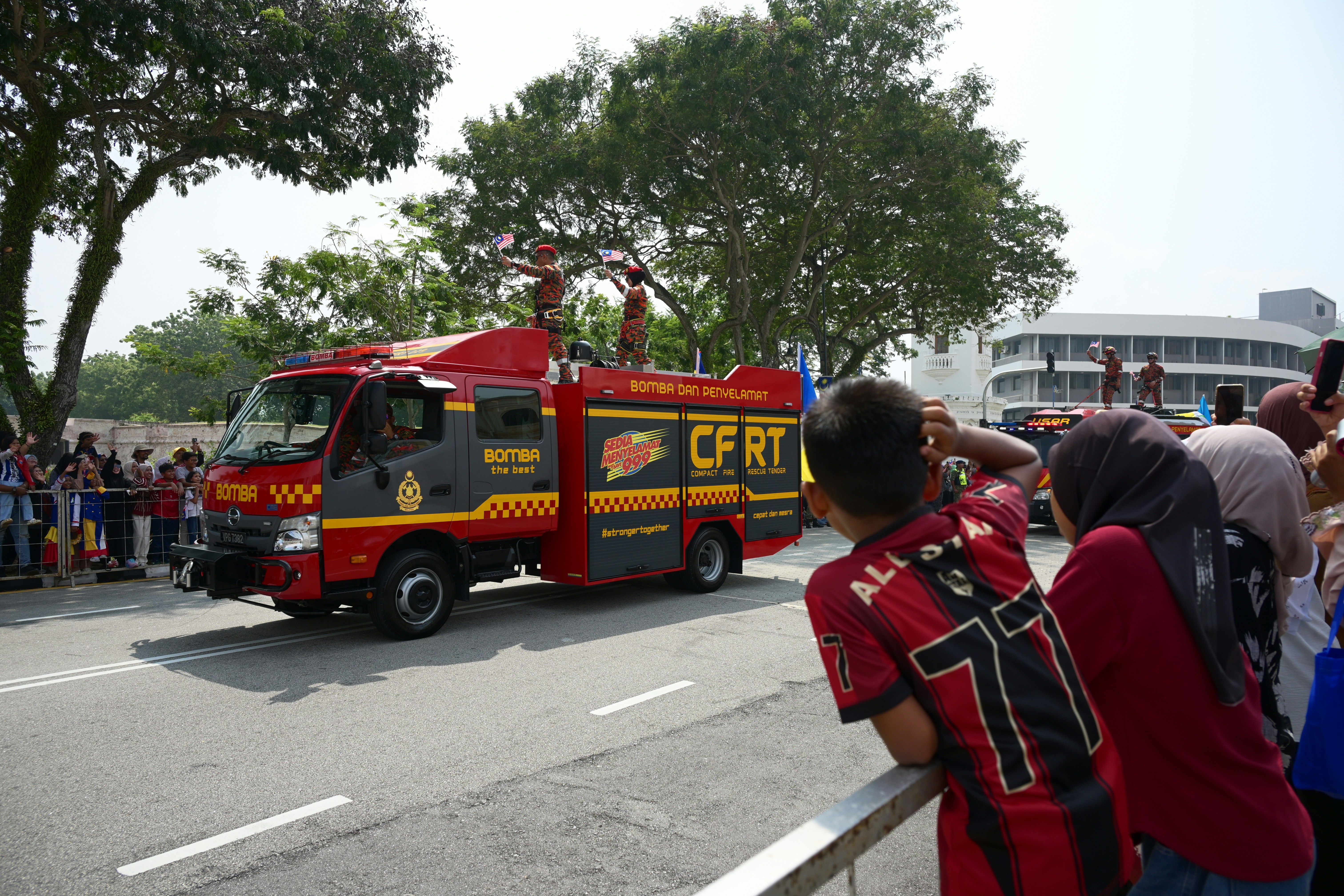 A bright red fire engine passes cheering spectators during the George Town Merdeka parade.