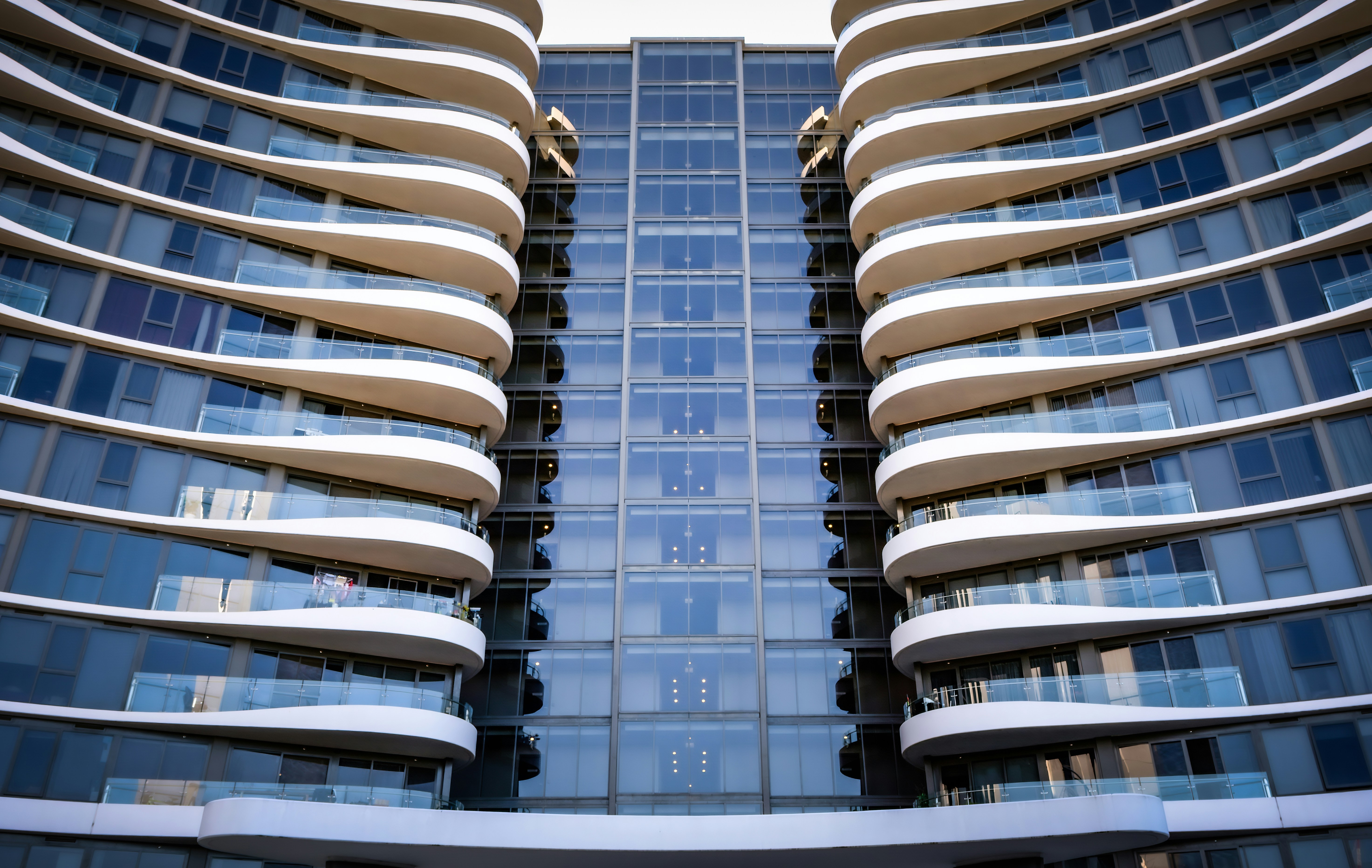 Twin-curved balconies frame a central glass atrium, creating a rhythmic, wave-like pattern across the building's façade.