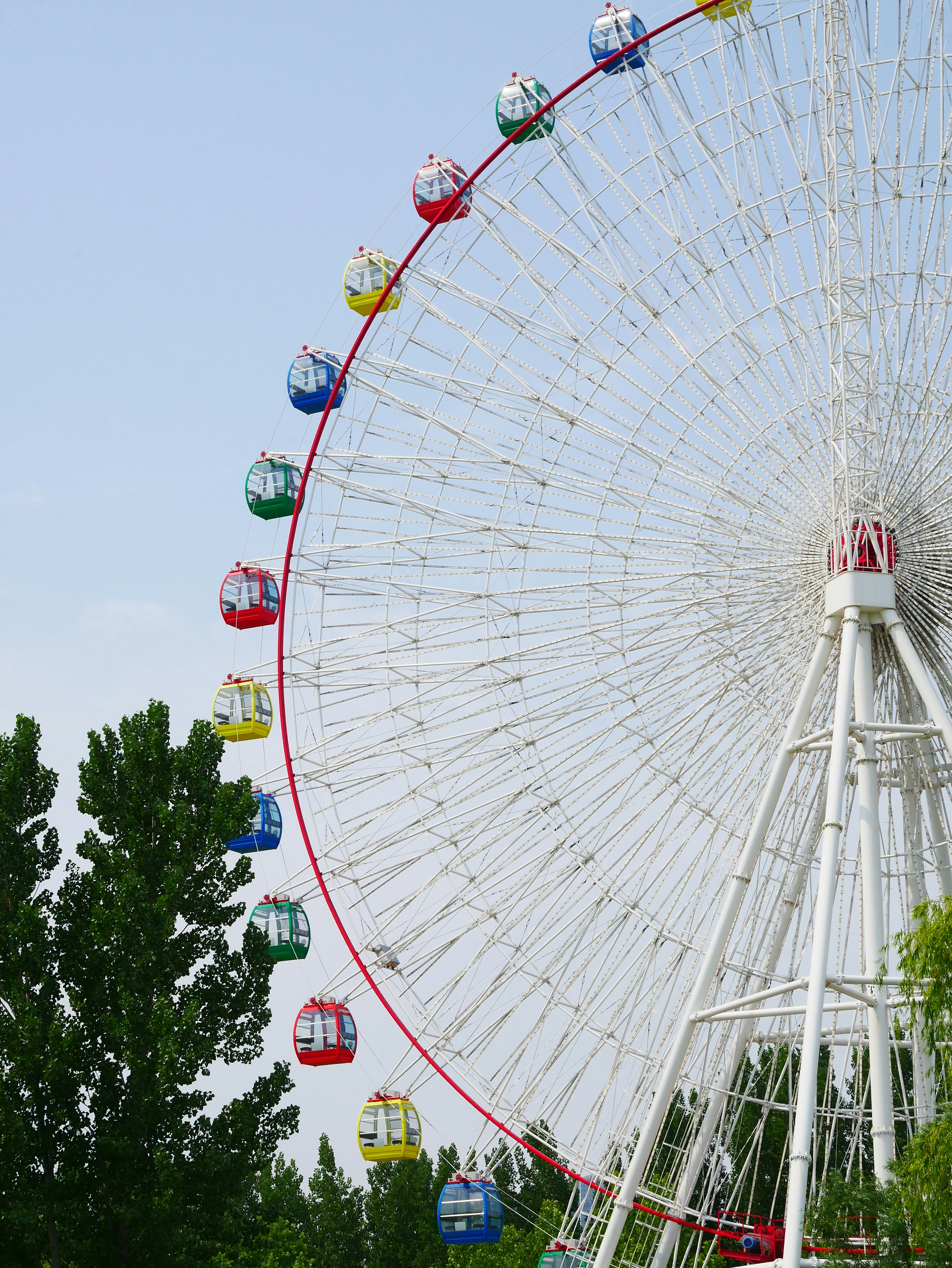Colorful Ferris wheel dominates the frame with green trees at the bottom and a pale blue sky above.