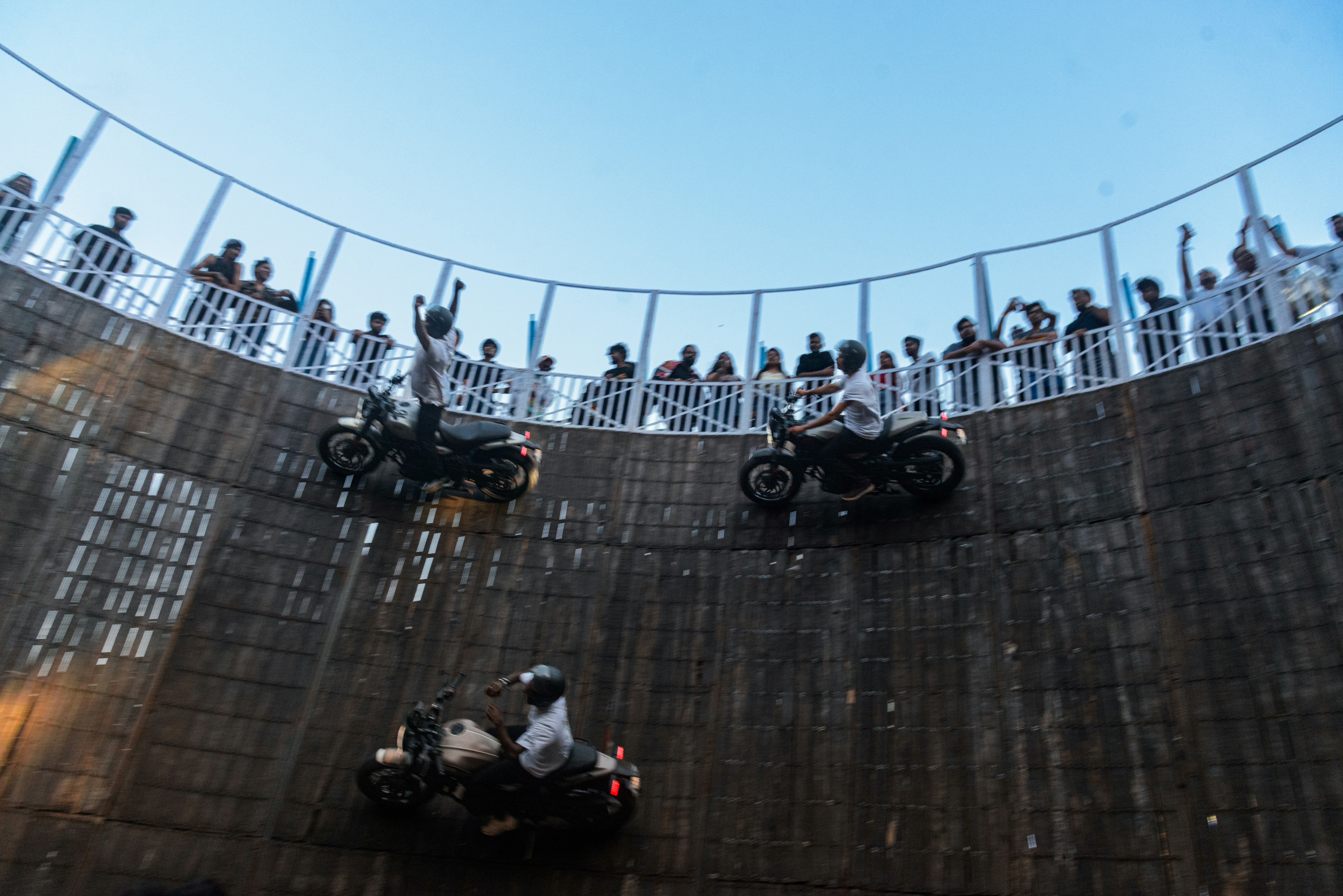 Motorbike riders defy gravity on a circular high‑wall while onlookers fill the rim
