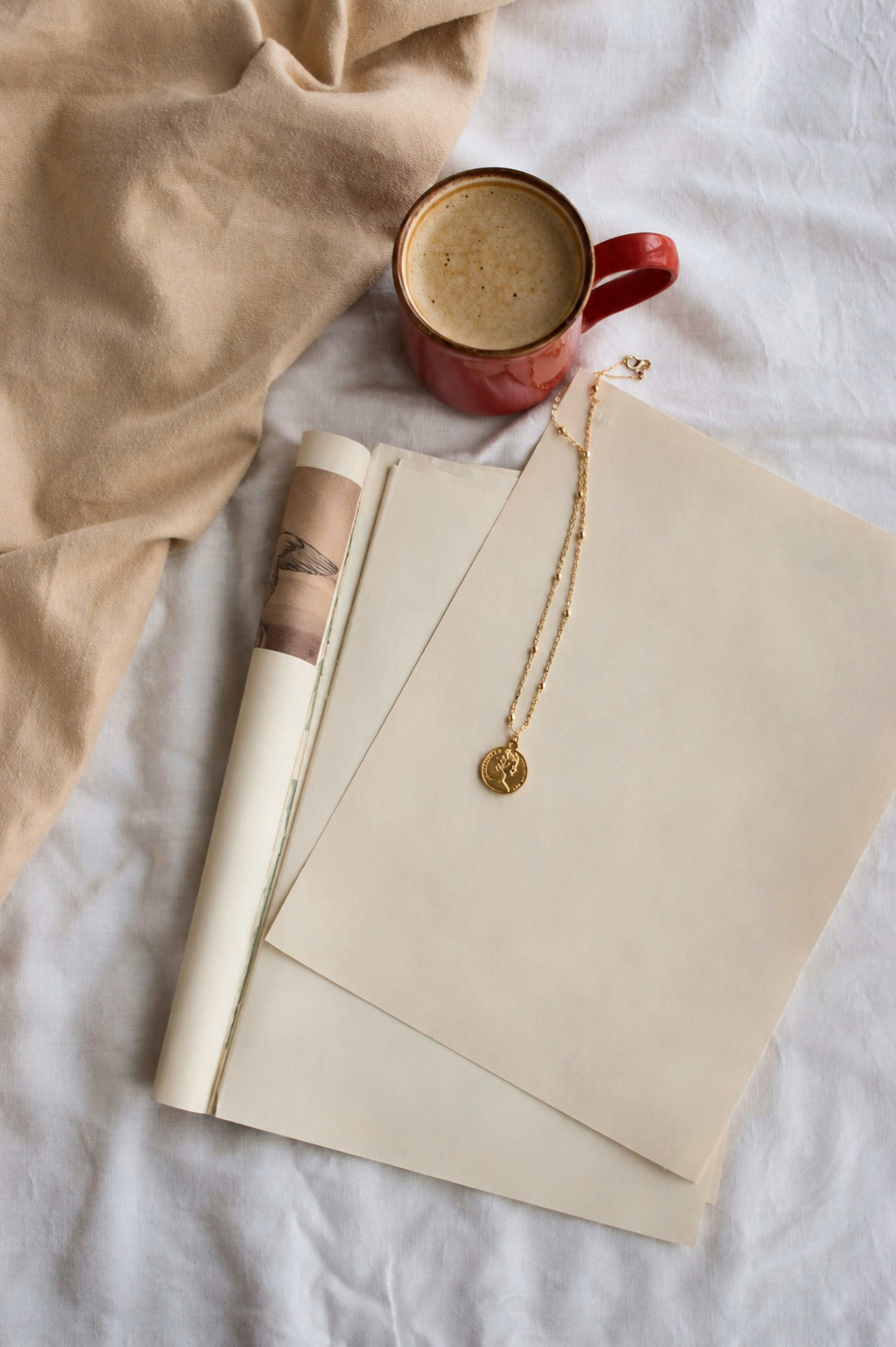 Champagne of mornings: a mug, necklace and papers laid to rest on a soft sheet