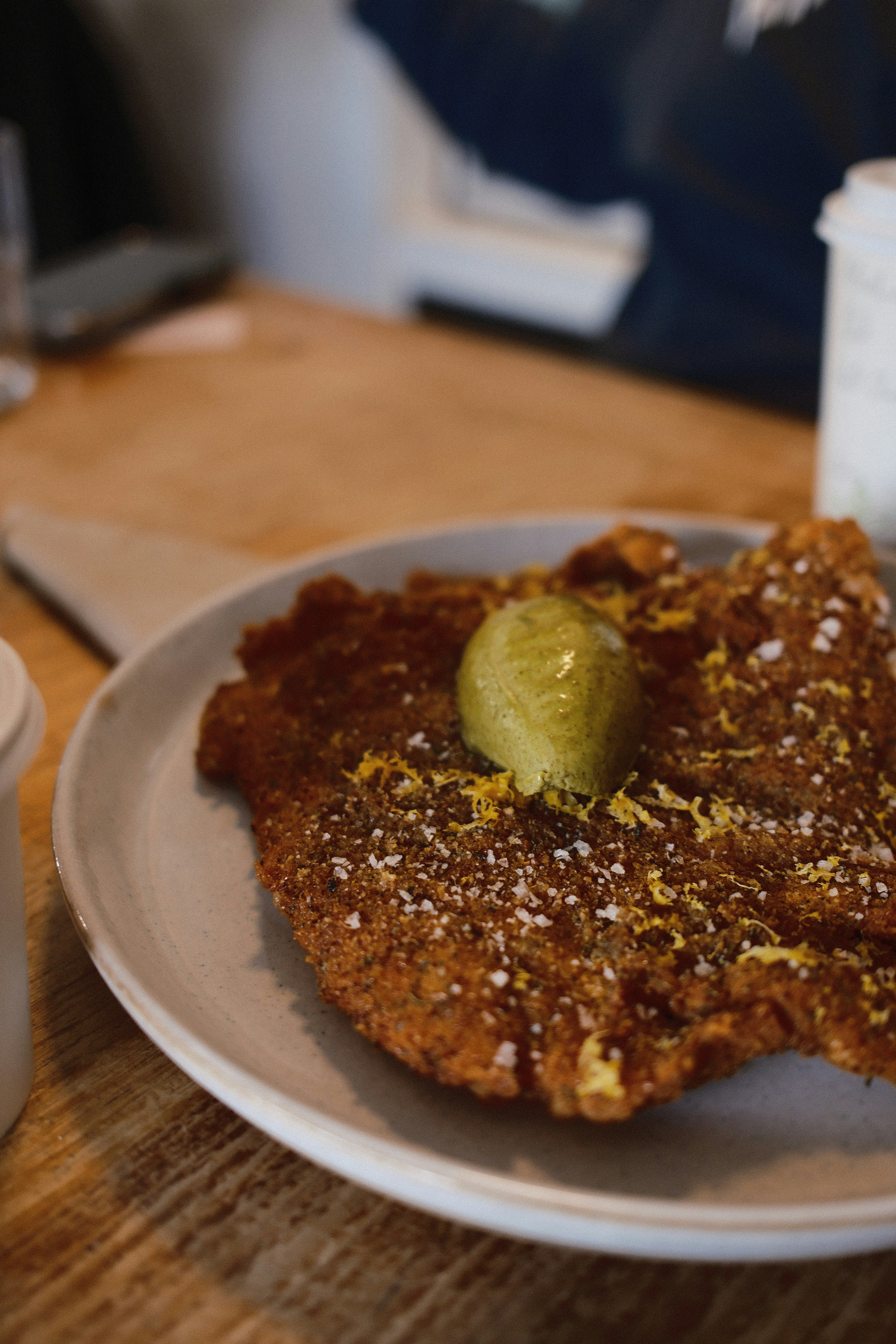 A breaded schnitzel topped with a scoop of herb butter and lemon zest