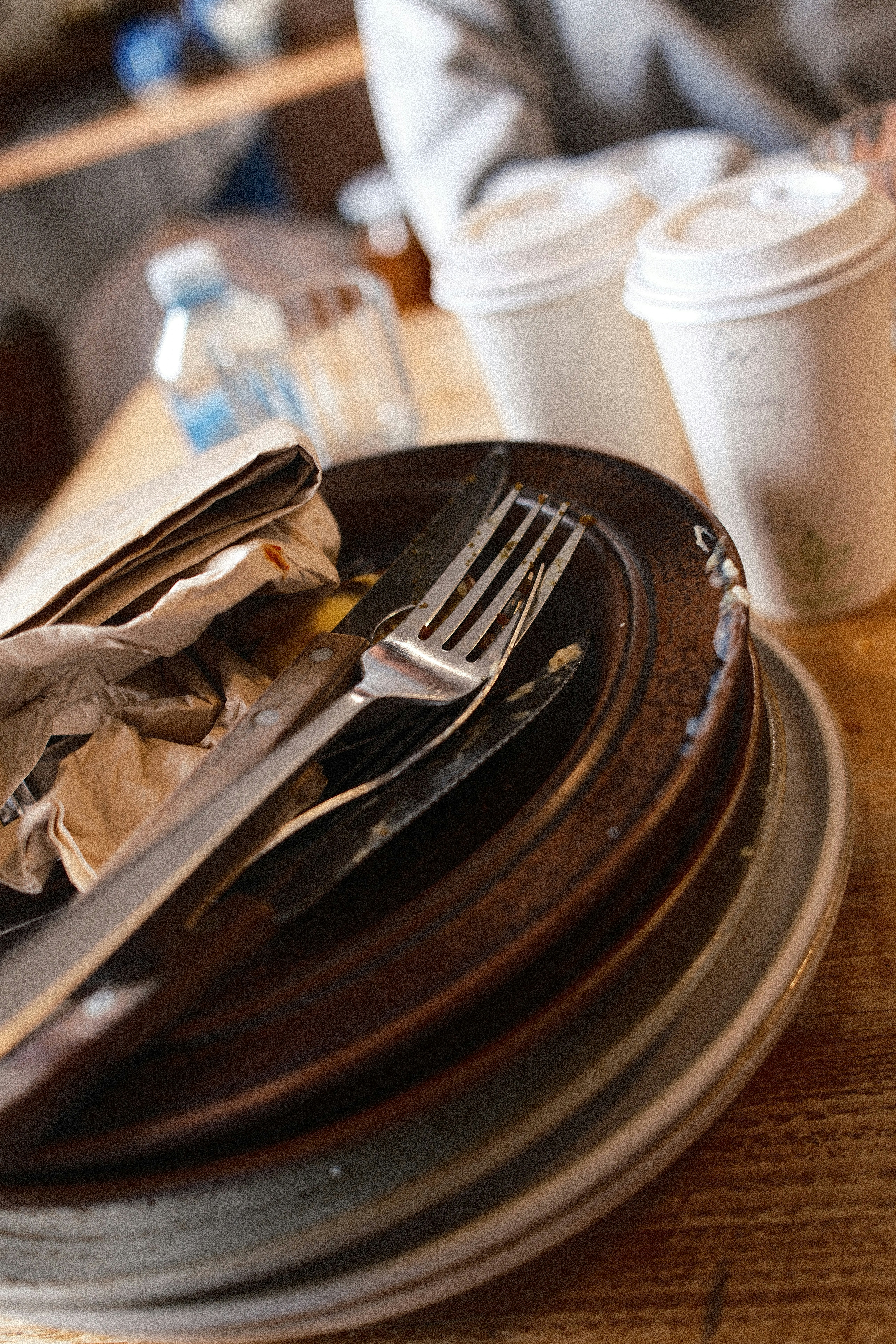 Messy dining scene: folded napkins and cutlery on stacked plates with takeout cups