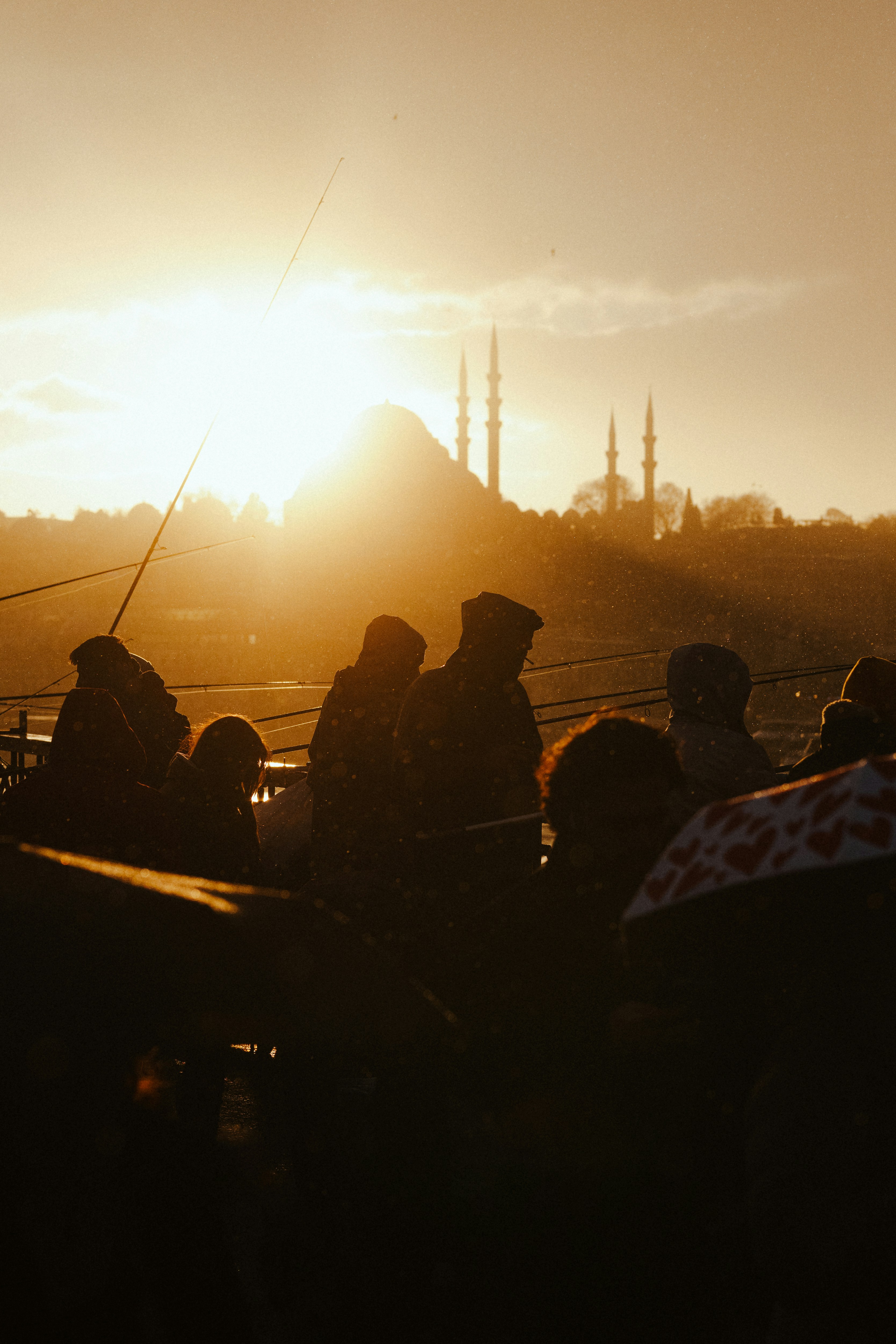 Hazy crowd silhouette against a warm sunset, with distant minarets rising above the skyline; a broad, atmospheric urban scene.